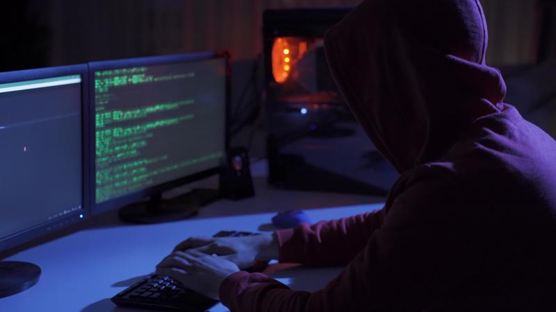 Side view of hacker sitting near computer monitors with green code screens. Lonely hacker ...