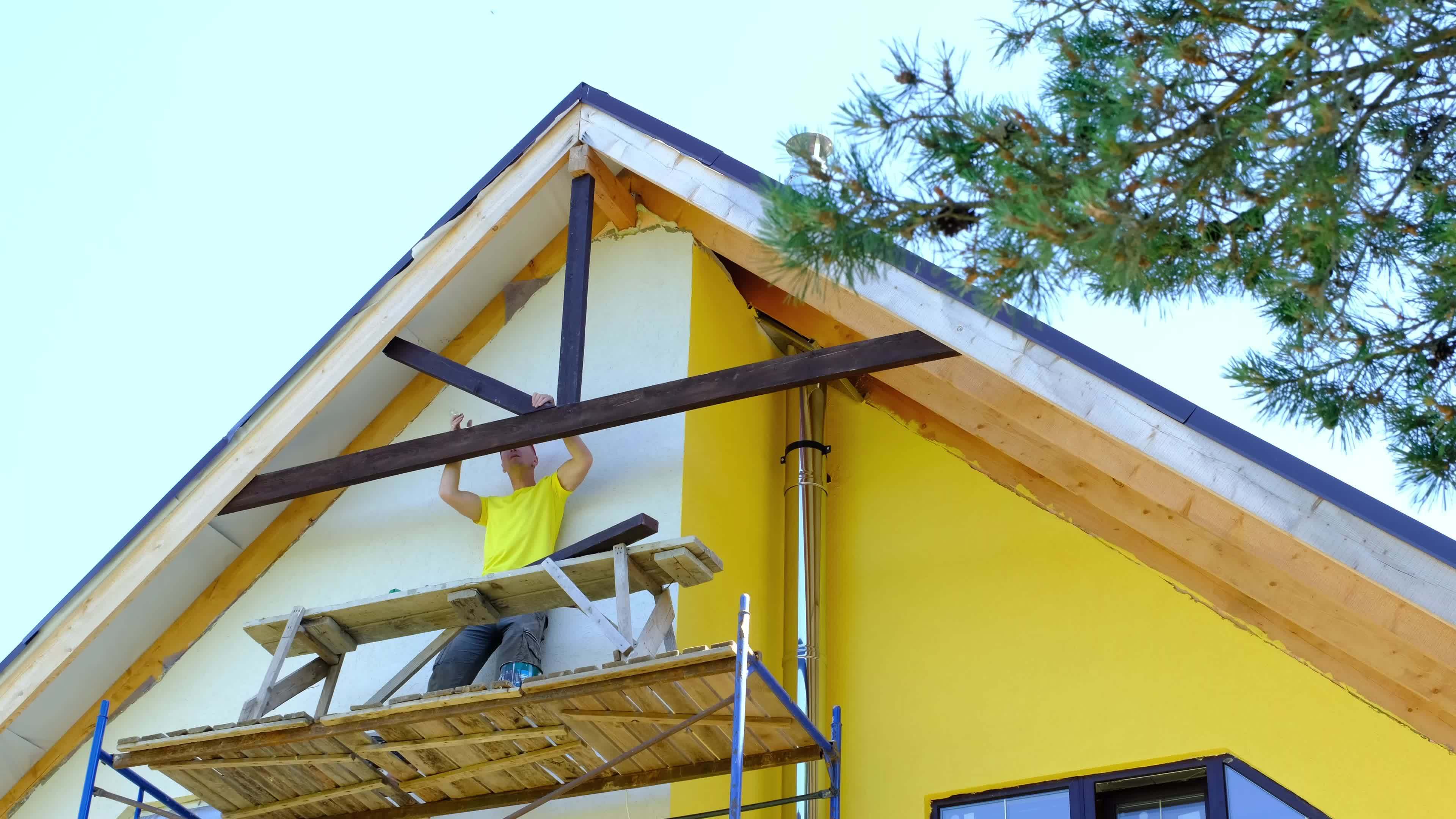 Male builder makes exterior decoration of private house in the style of half-timbered house with ...
