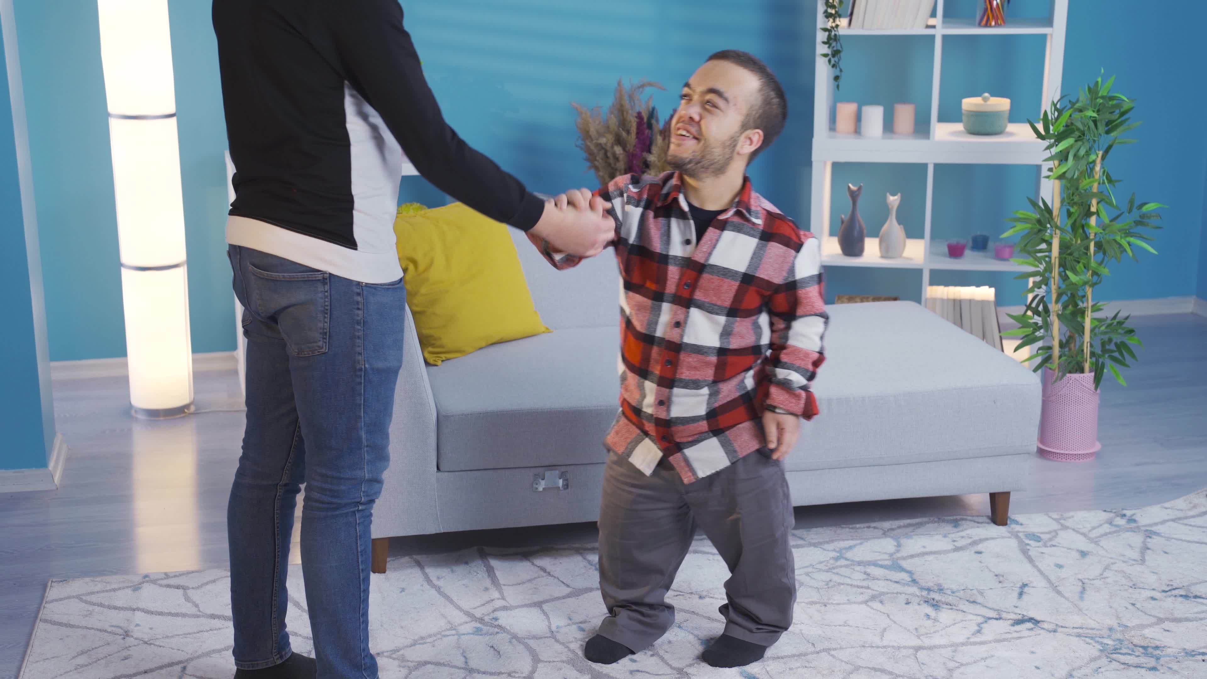 Young man with dwarfism chatting and greeting with his close male friend at home. A young man ...