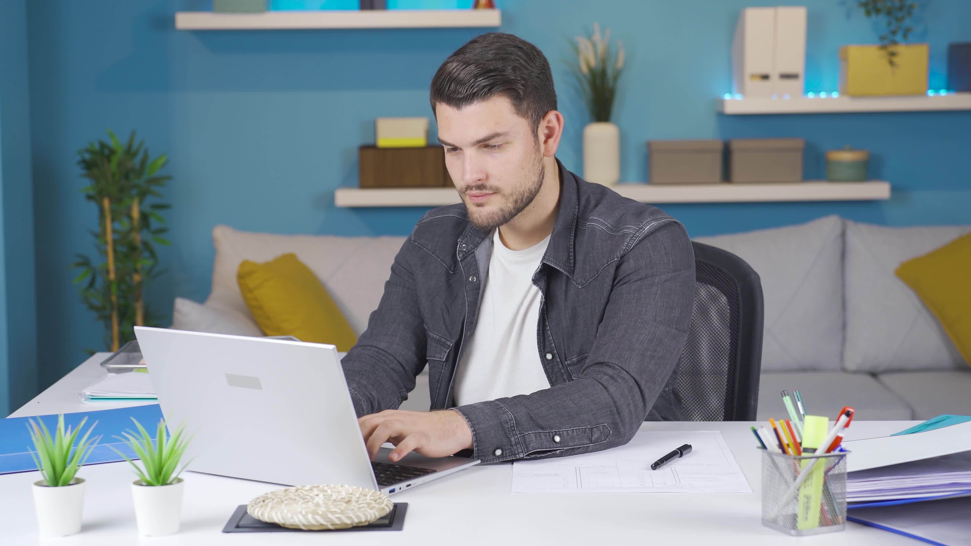 Man working from laptop smiles looking at camera. Young man using ...
