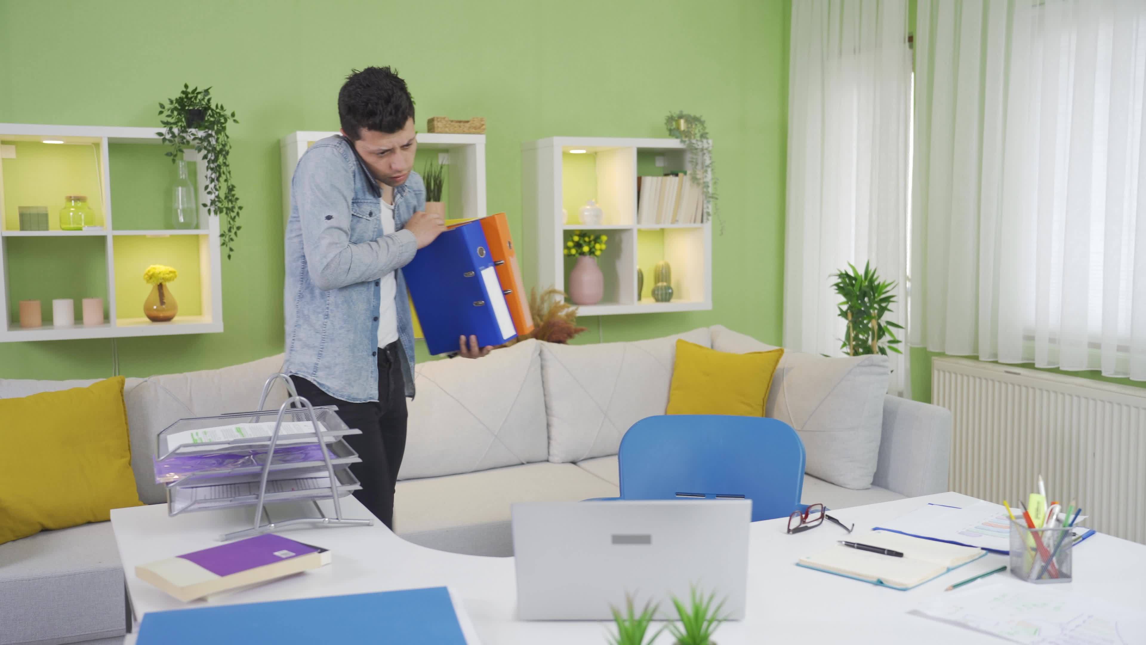 Clumsy young man drops file folders while working from home. Distracted ... Clumsy young man drops file folders while working from home. Distracted ...