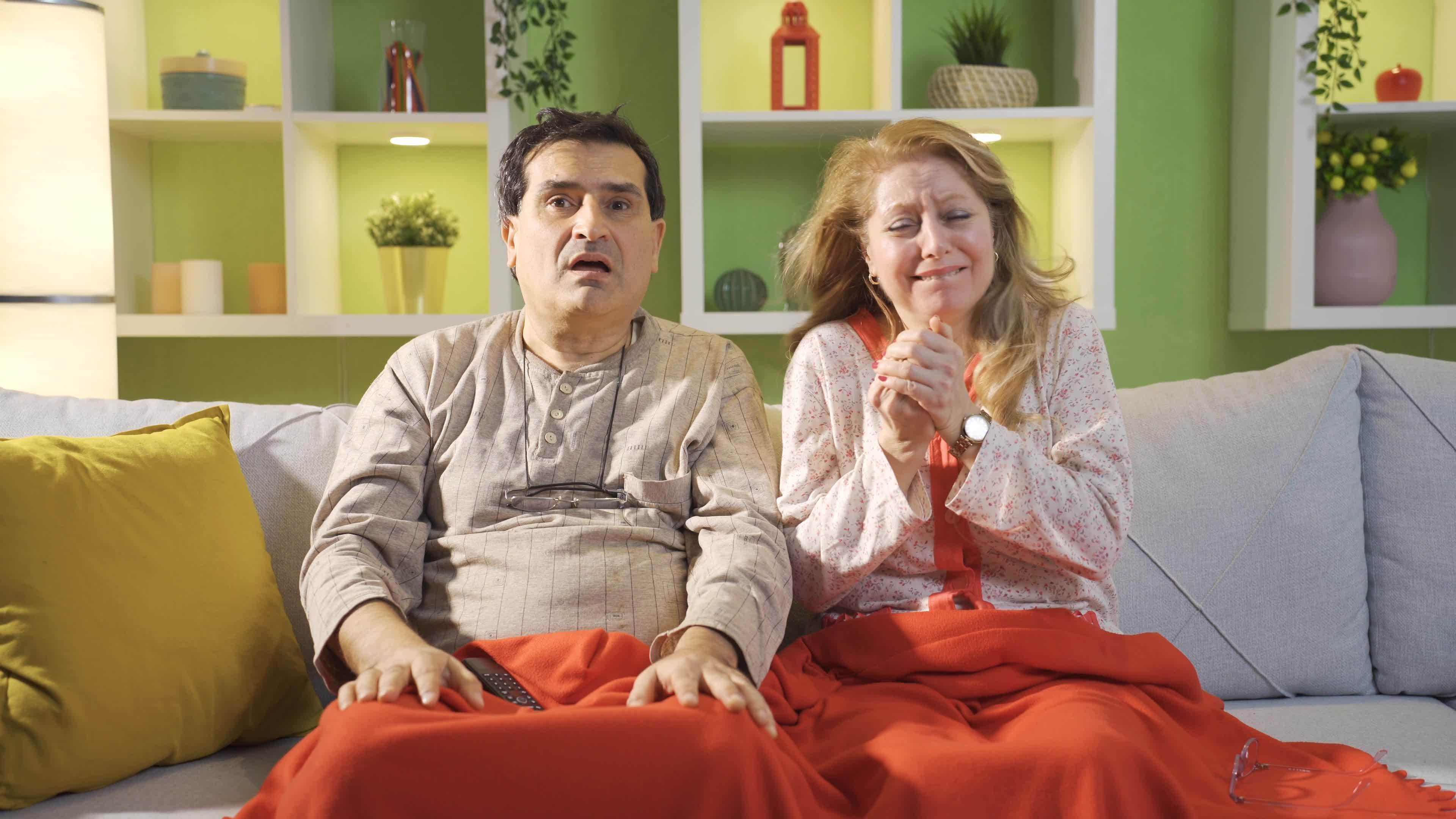 Couple watching horror and thriller movies on TV alone at home. Scared married couple watching ...