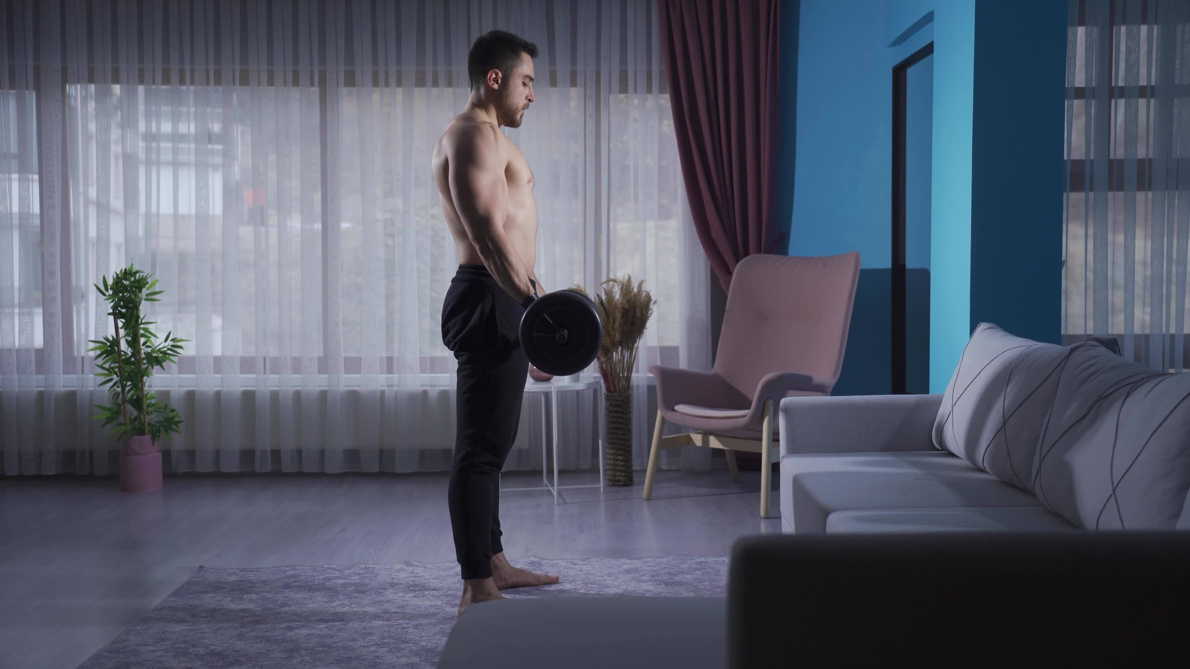 Young athlete working harder to grow his muscles. Exercising at home. The young athlete is ...