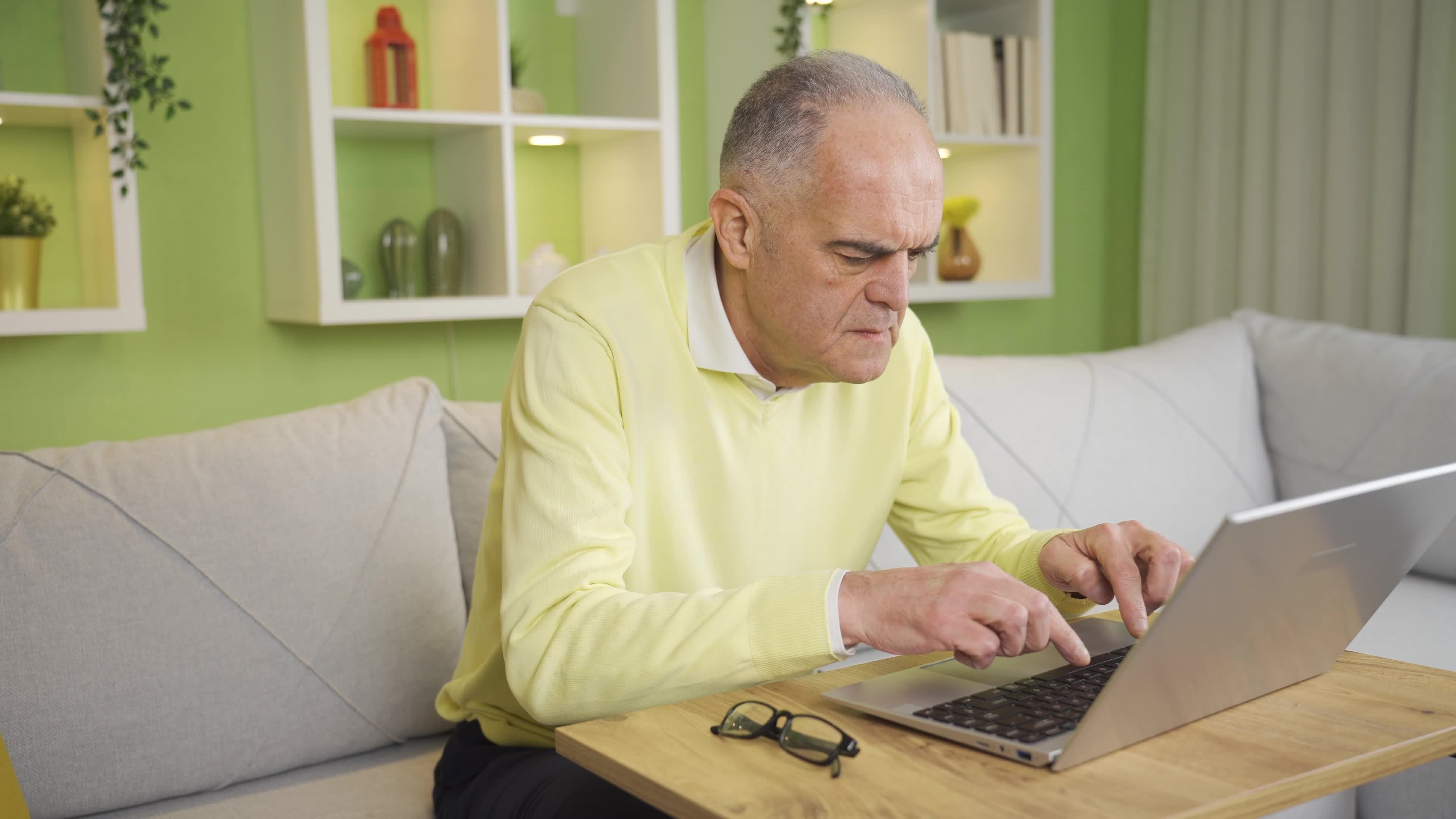Elderly retired man using laptop at home, wearing his glasses. The old ...