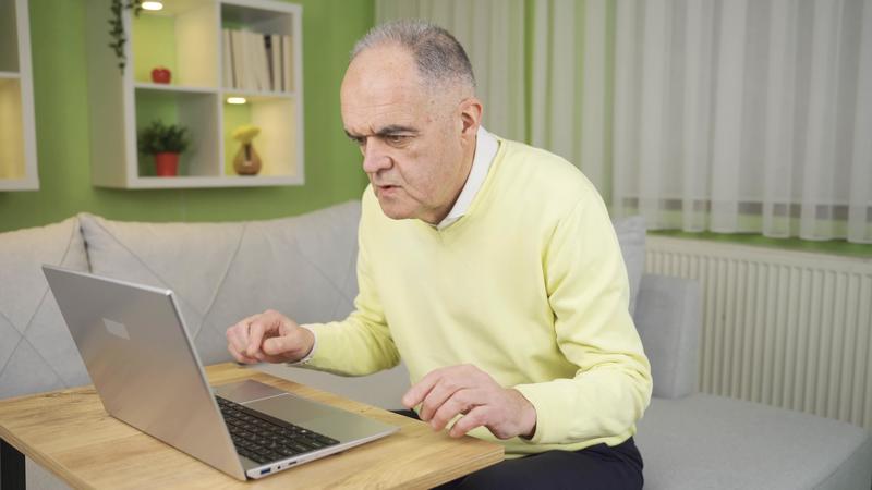 The bewildered old man. Retired old man using laptop at home is ...