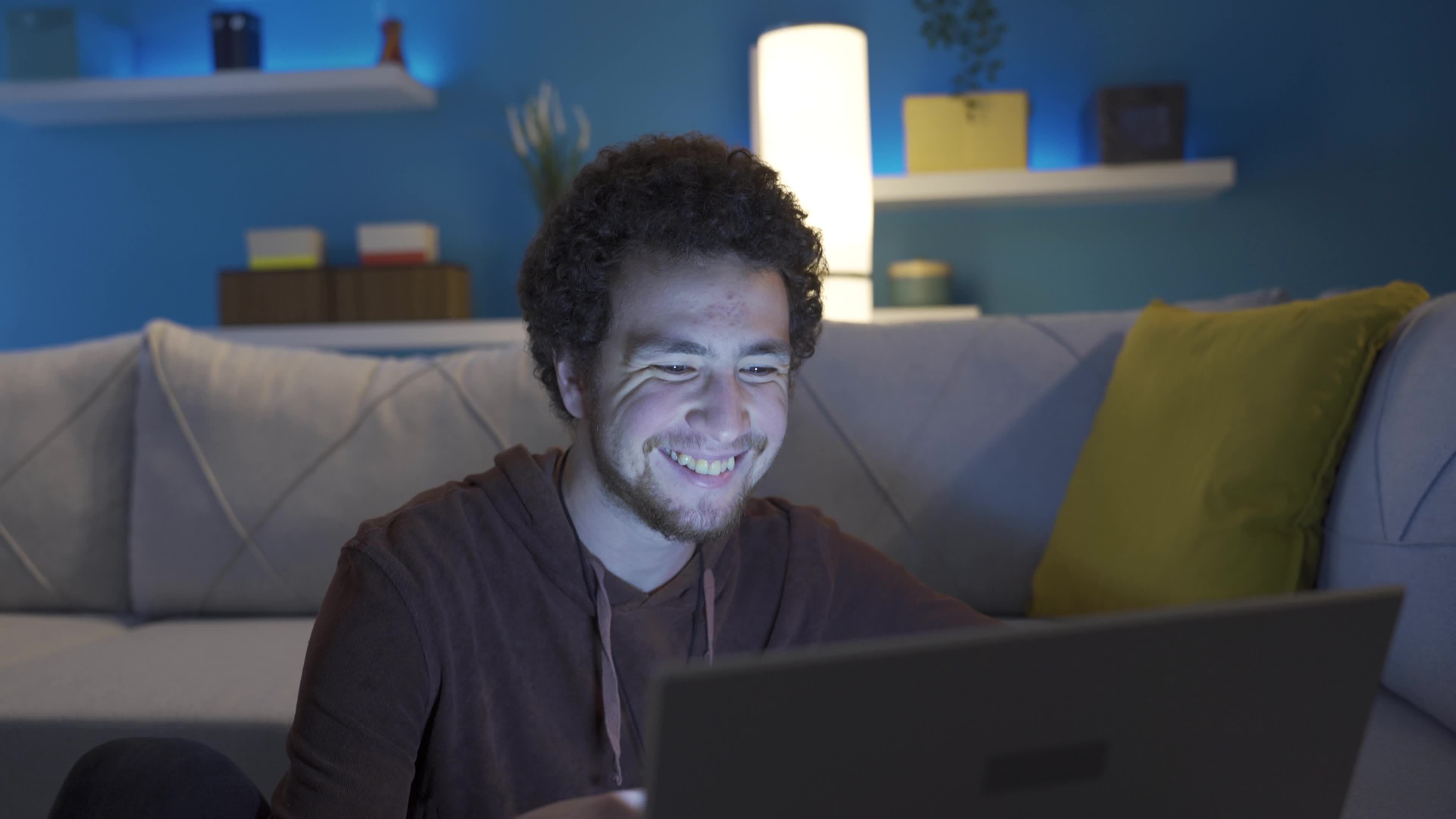 Young man smiling in the face of what he sees on the laptop screen. The ...