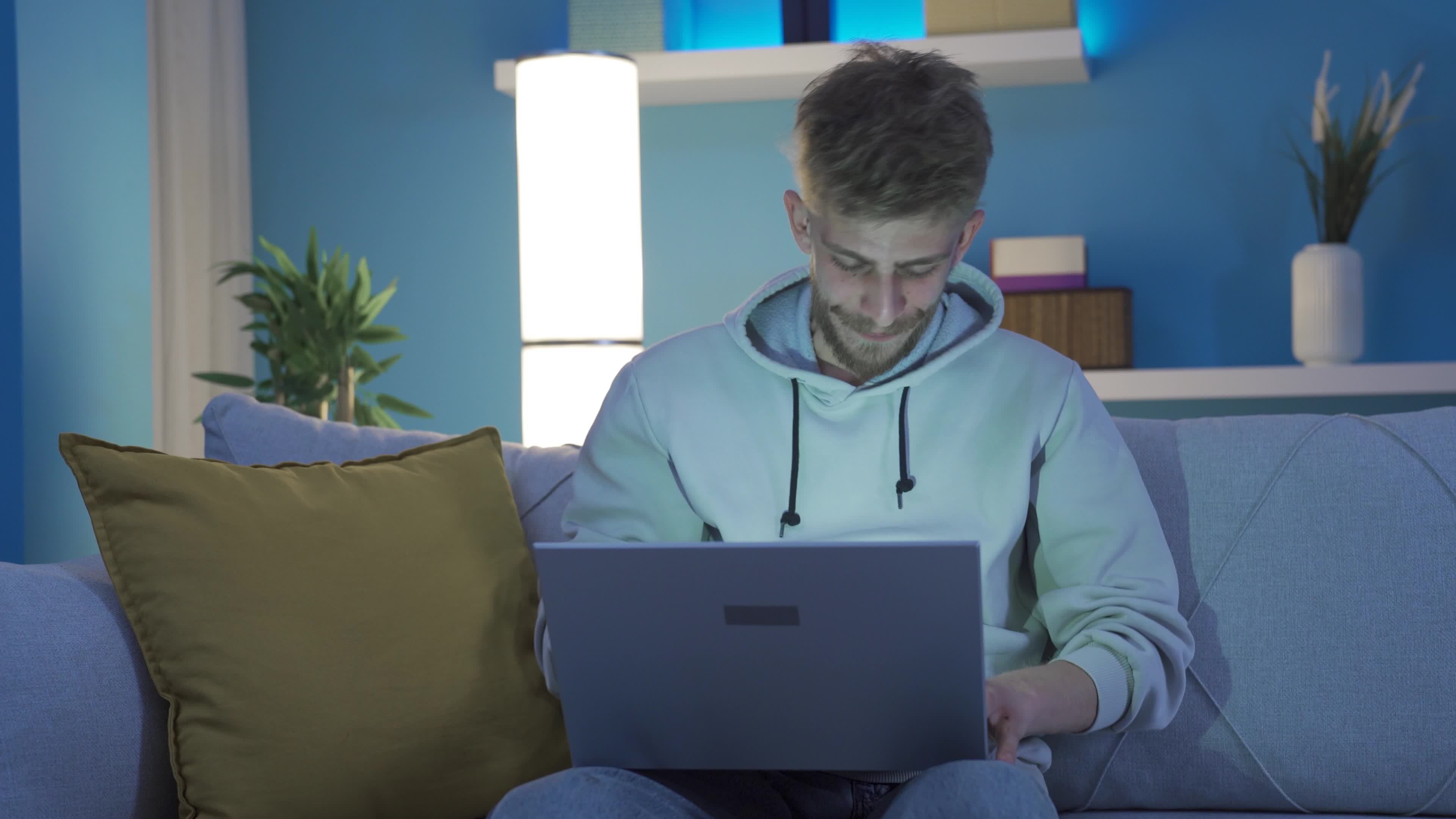 Positive cute and handsome young man is using laptop at home, in ...