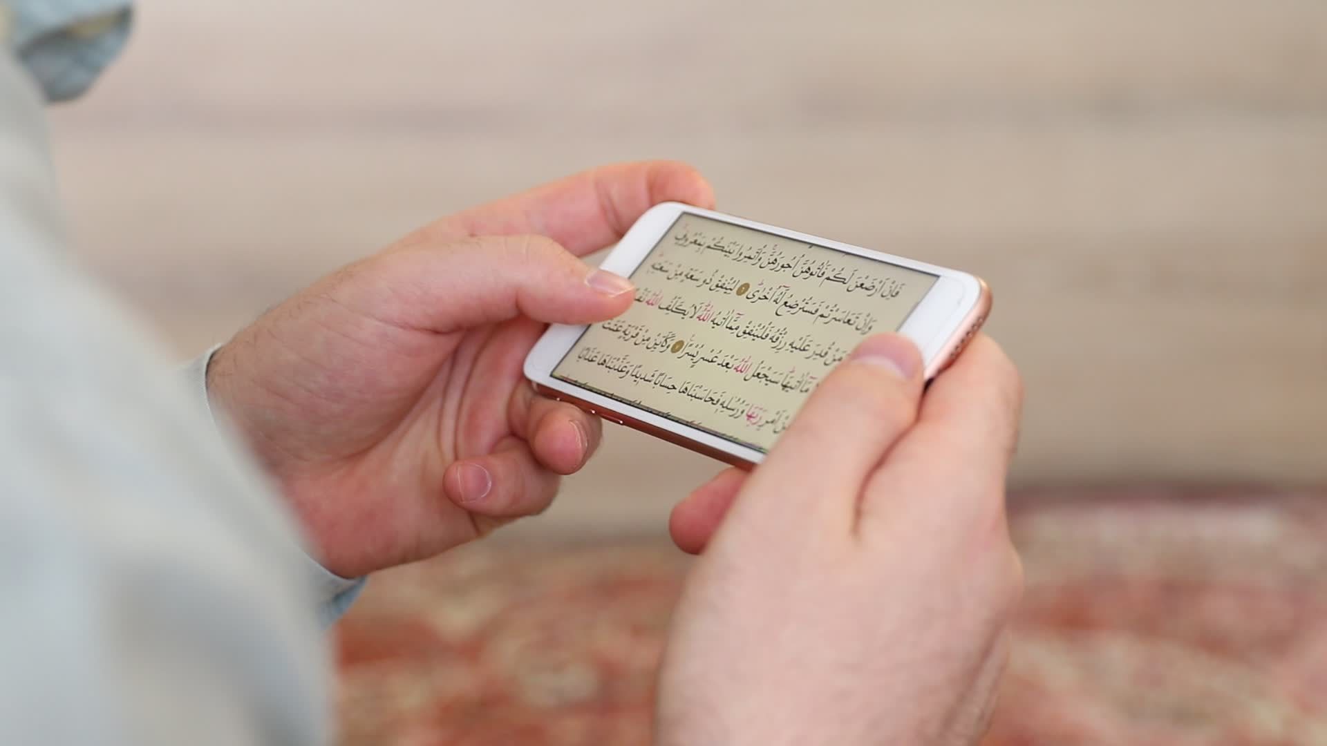 Quran open on the screen of the phone he is holding, the alphabet of the religious book of Islam ...