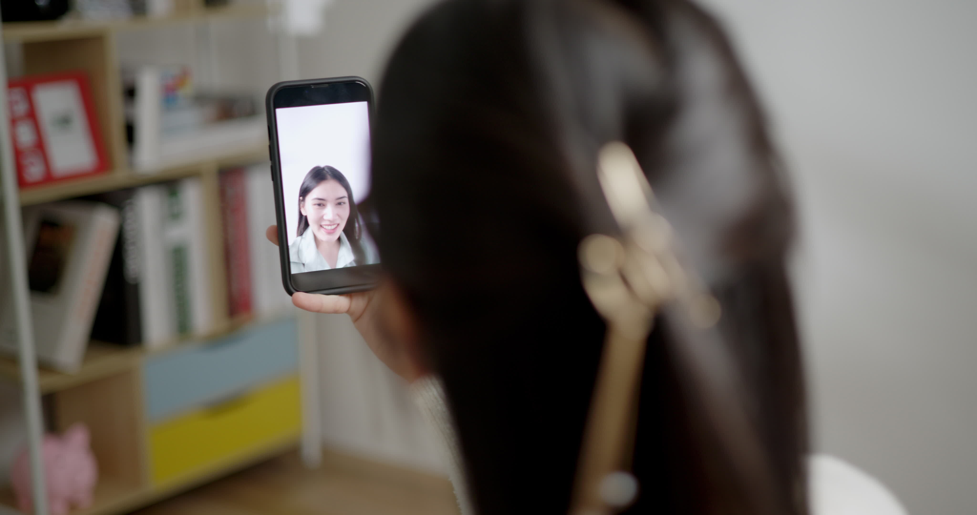 Handheld shot, Selective focus, Rear view of Young woman with eyeglasses holding smartphone ...