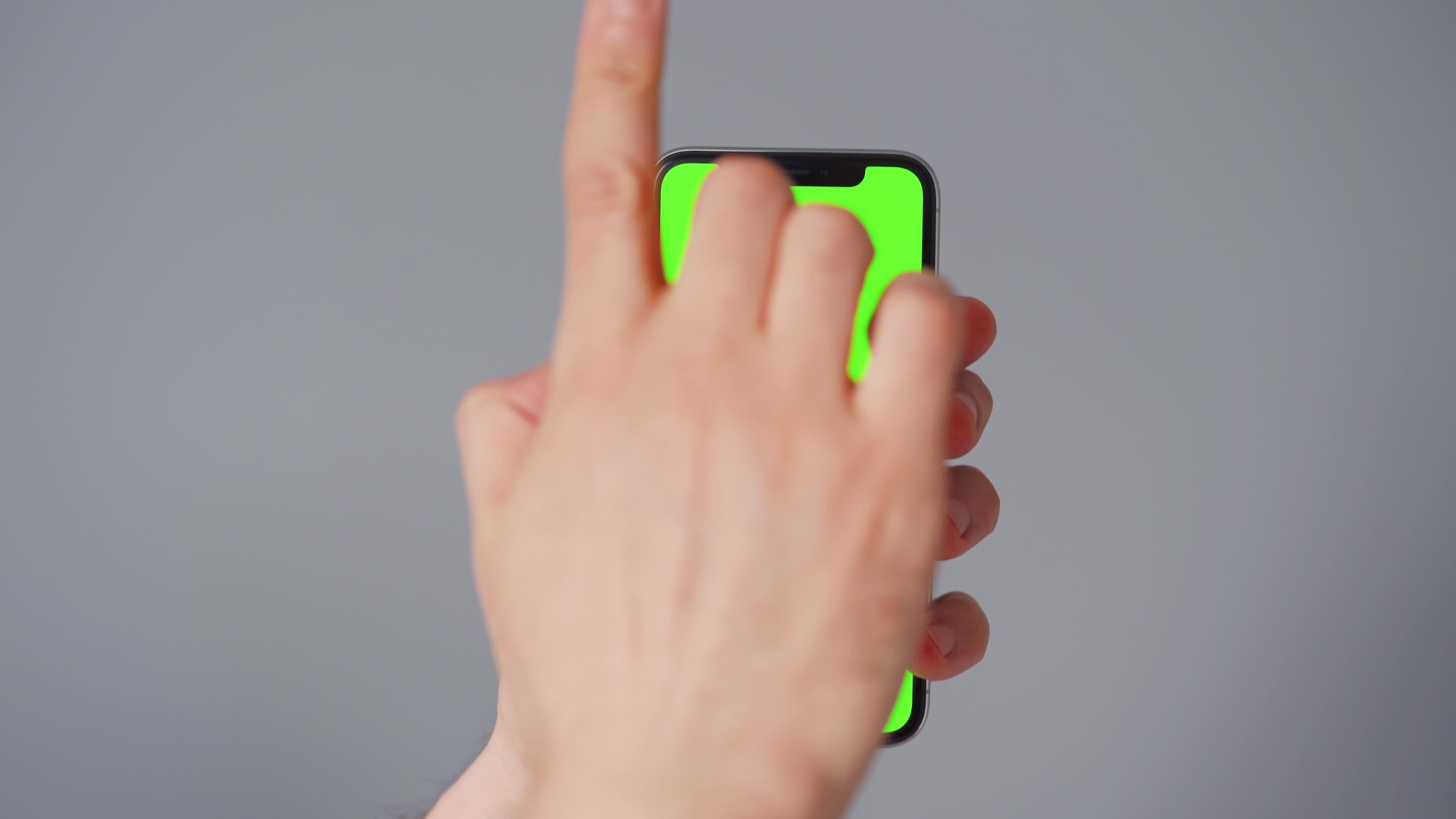 Male hands using a smartphone with a green screen on a gray background close-up. Chroma key ...