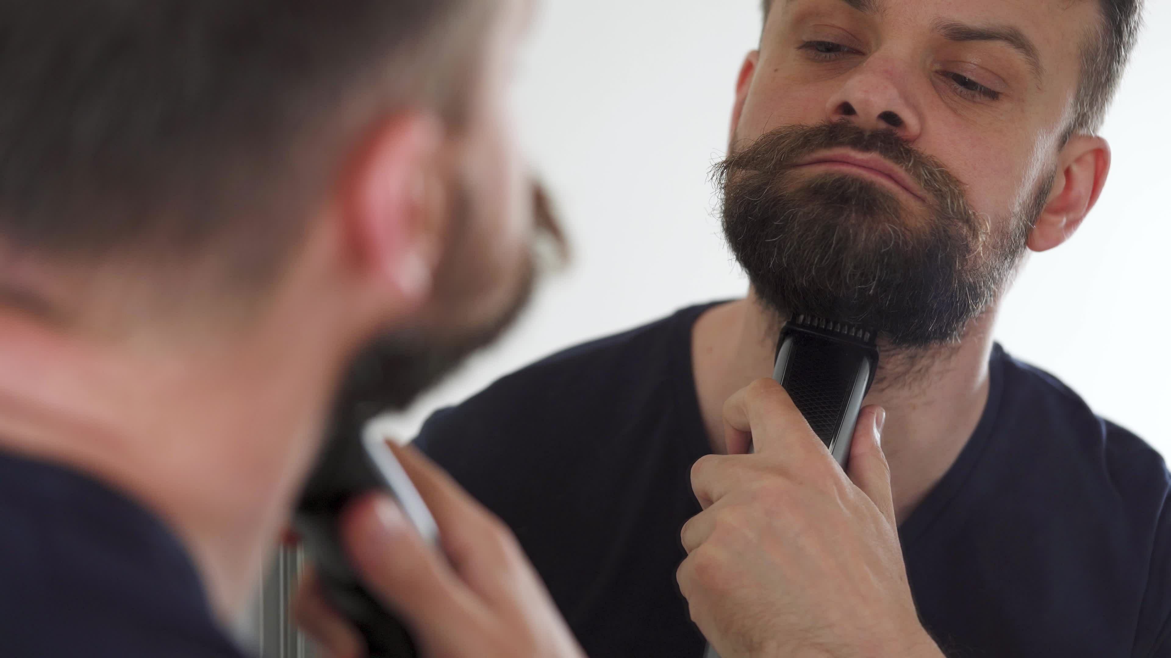 Man shaves his beard using an electric trimmer. Morning routine ...