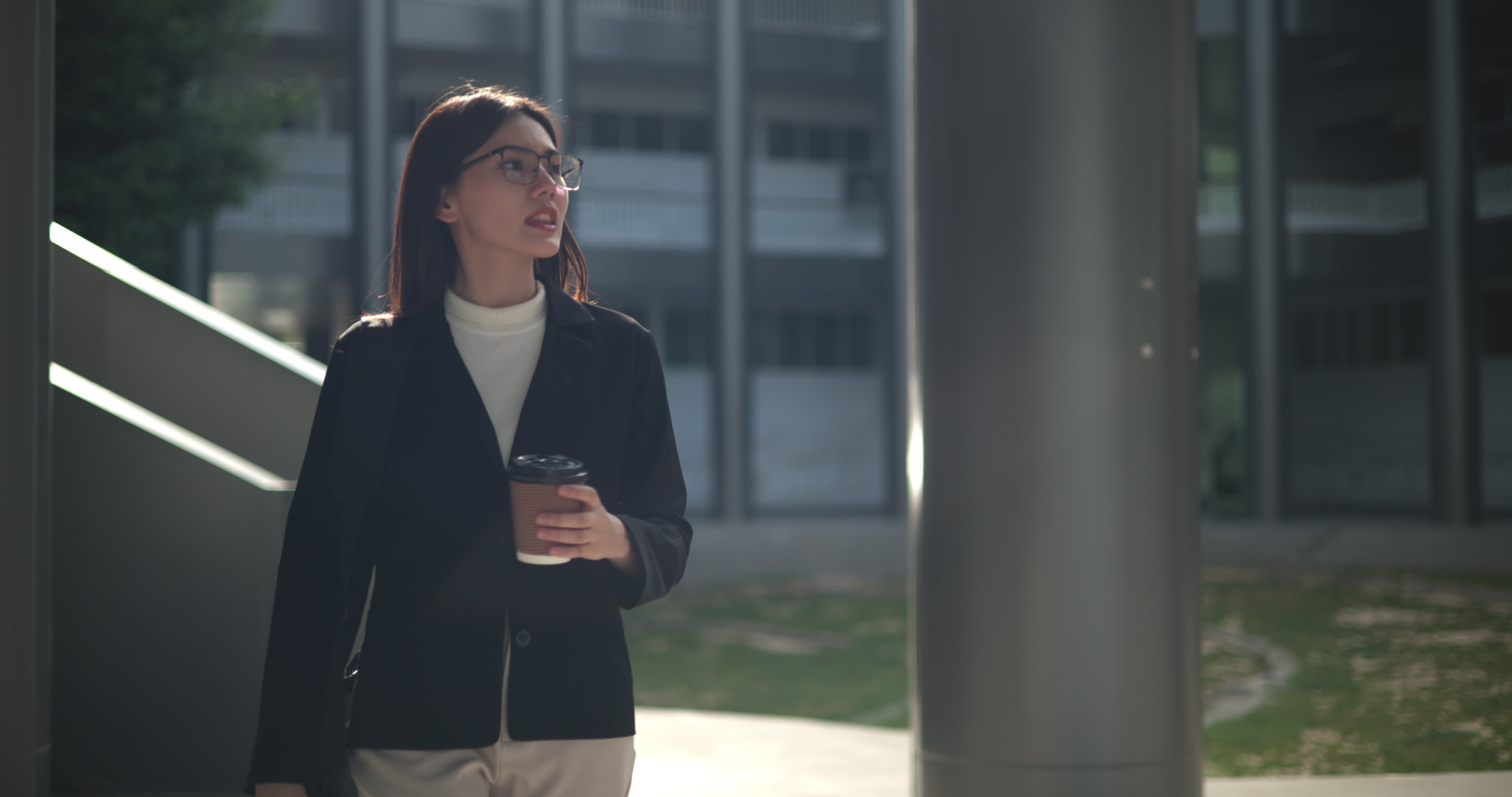Footage of Young elegant Asian busy businesswoman wearing glasses in a suit holding a cup of ...
