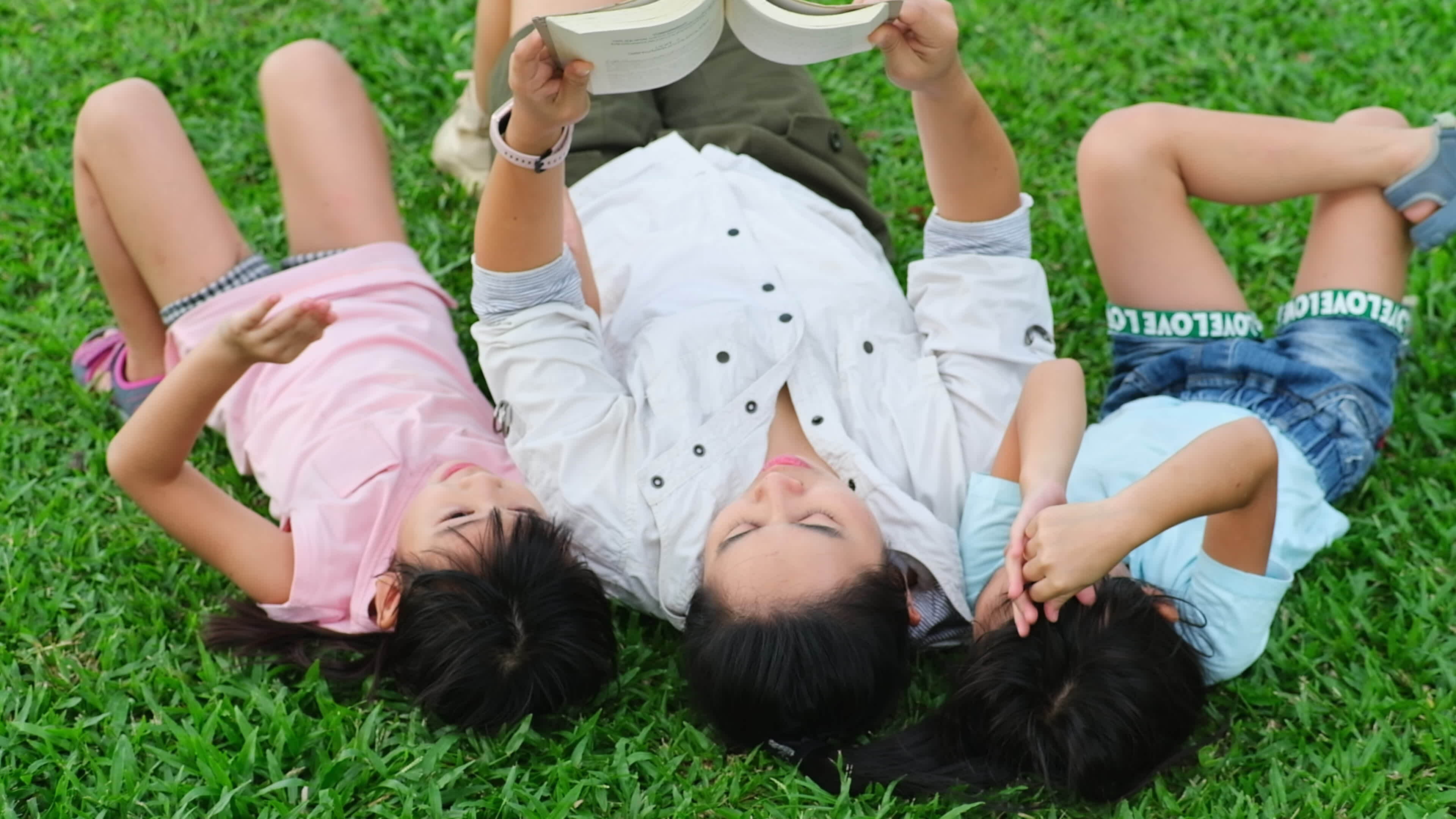 Happy mother and two daughters having fun and enjoying reading at the park. Mother and daughter ...
