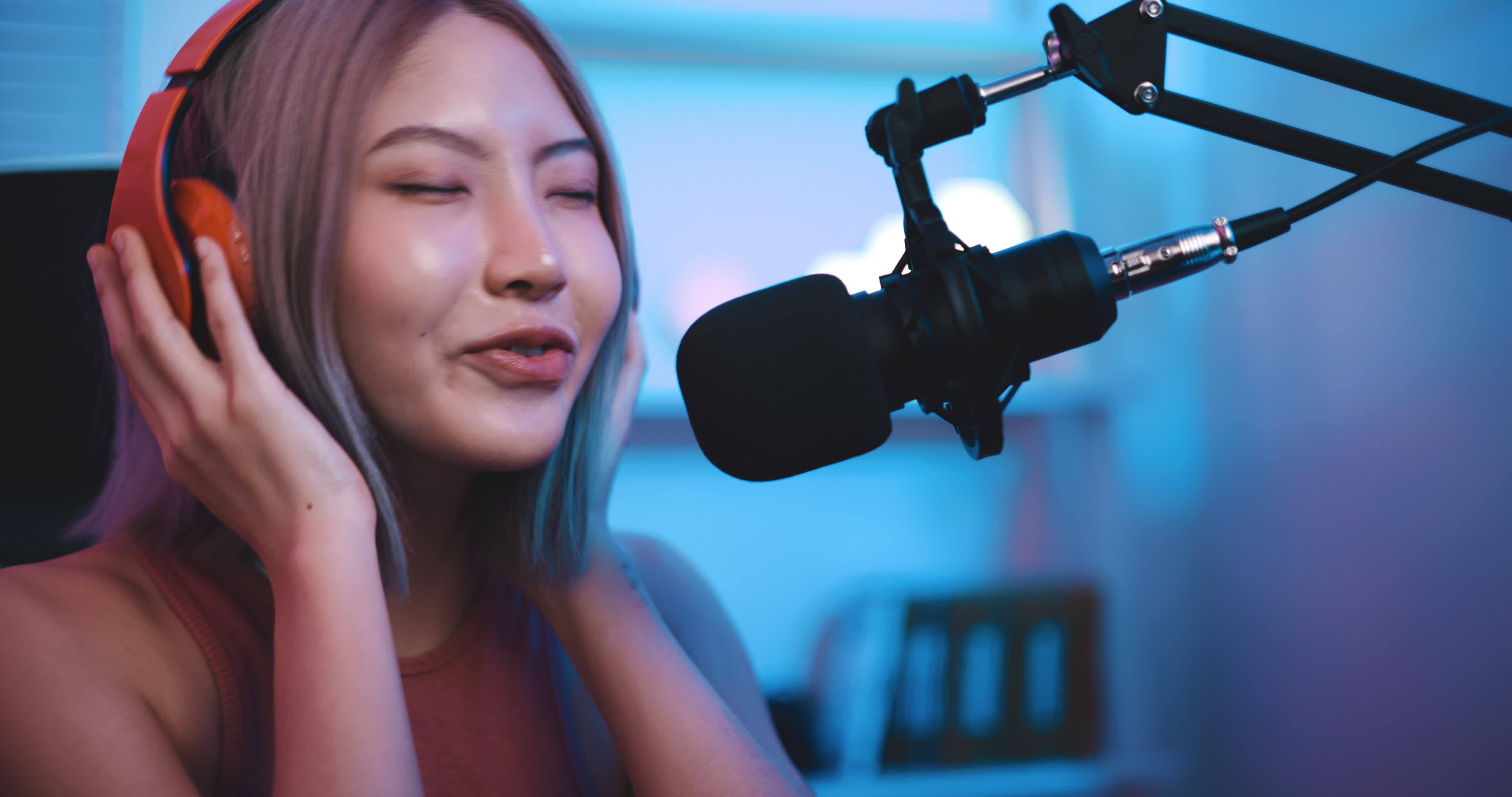 Footage of Young Asian woman influencer wearing headphones talking into a microphone while ...