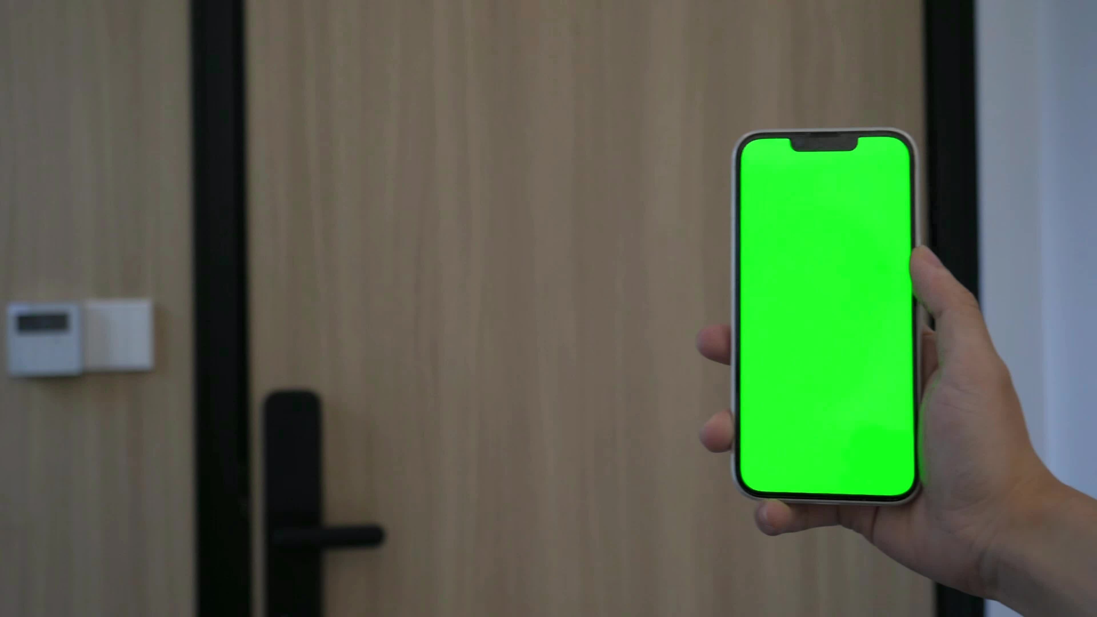 Male hand using a smartphone with a green screen on a brown background close-up. Chroma key pro ...