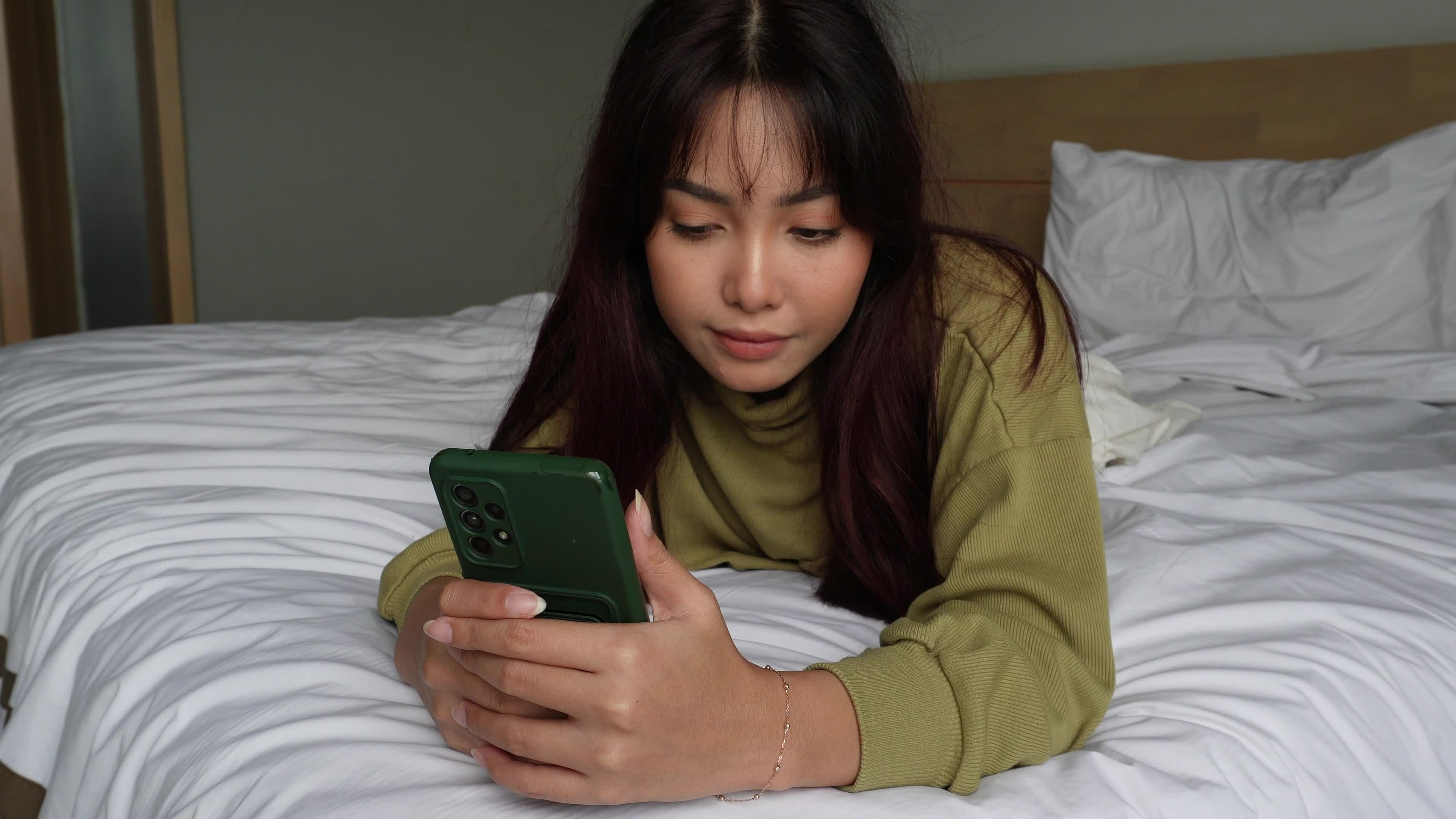Asian woman laying on bed while scrolling on her phone 28093658 Stock Video at Vecteezy