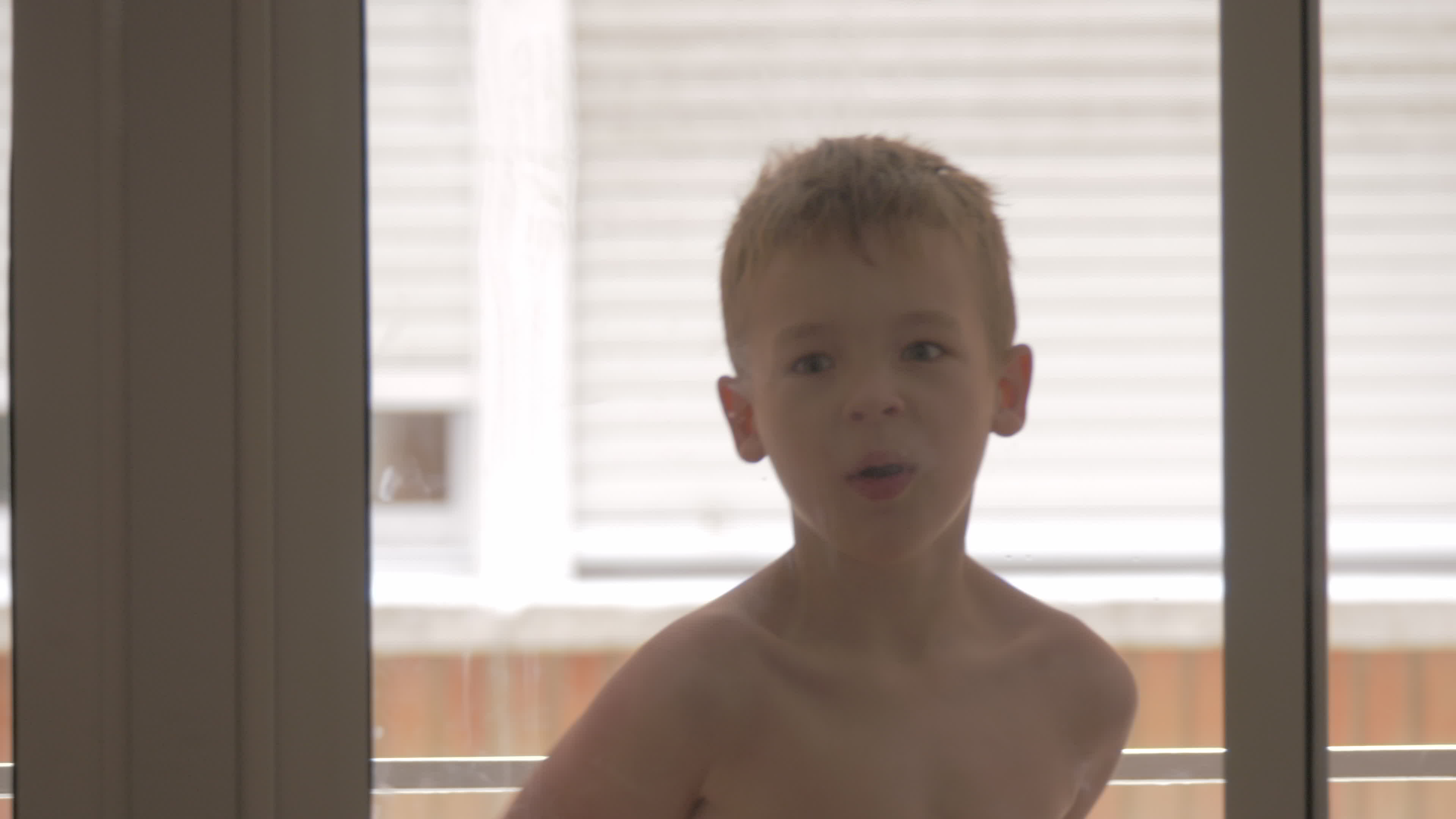 Funny kid fooling with towel and having fun, view through the glass 28744849 Stock Video at Vecteezy