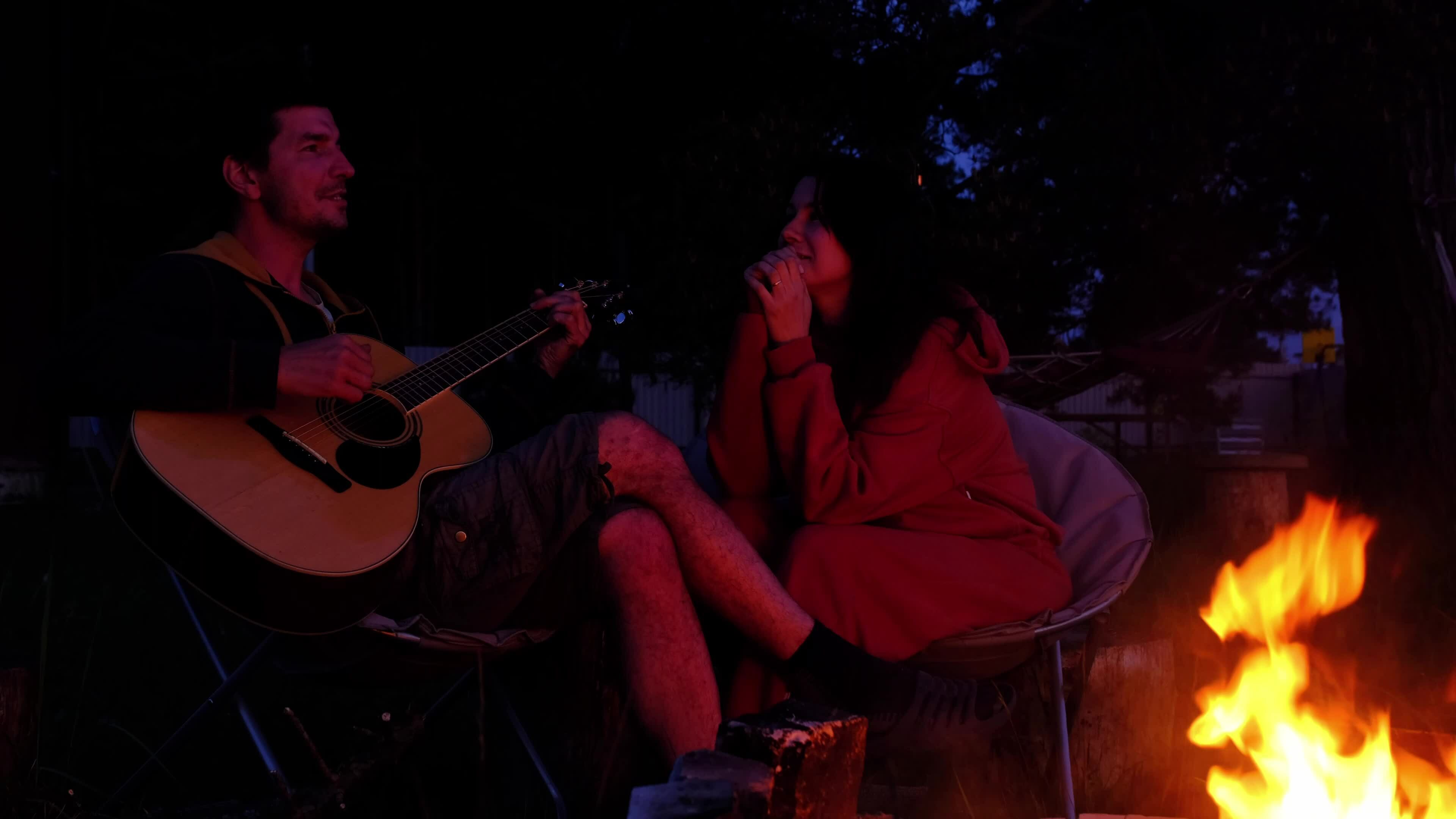 A man plays the guitar, a woman listens and sings along. A couple in love is sitting by the ...