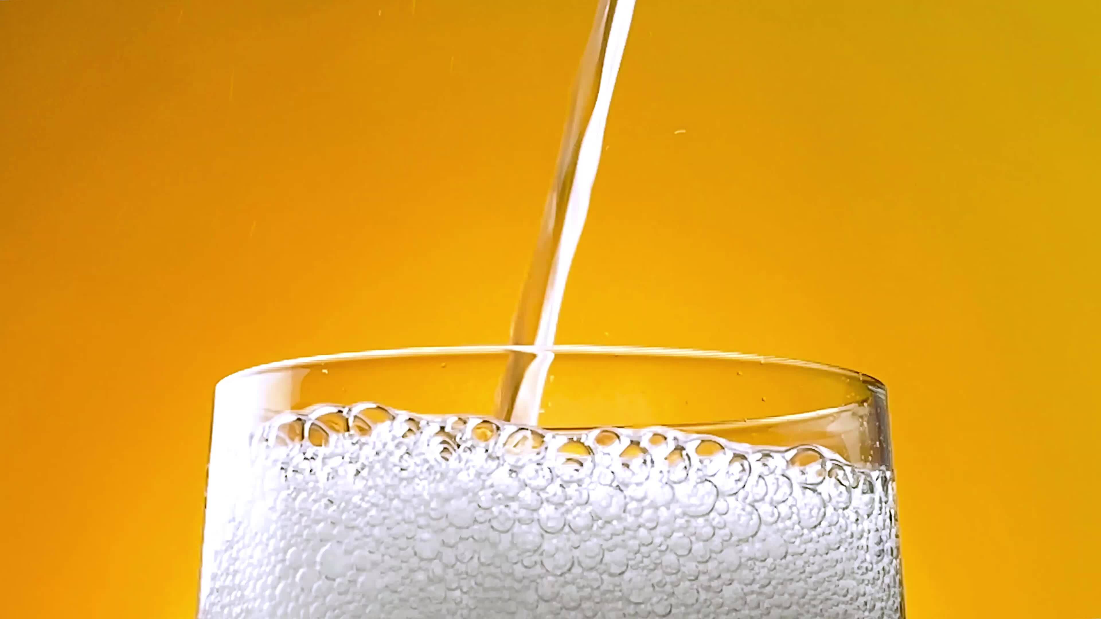 Pouring carbonated water into a glass. Yellow orange background, slow motion video. Bubbles in ...