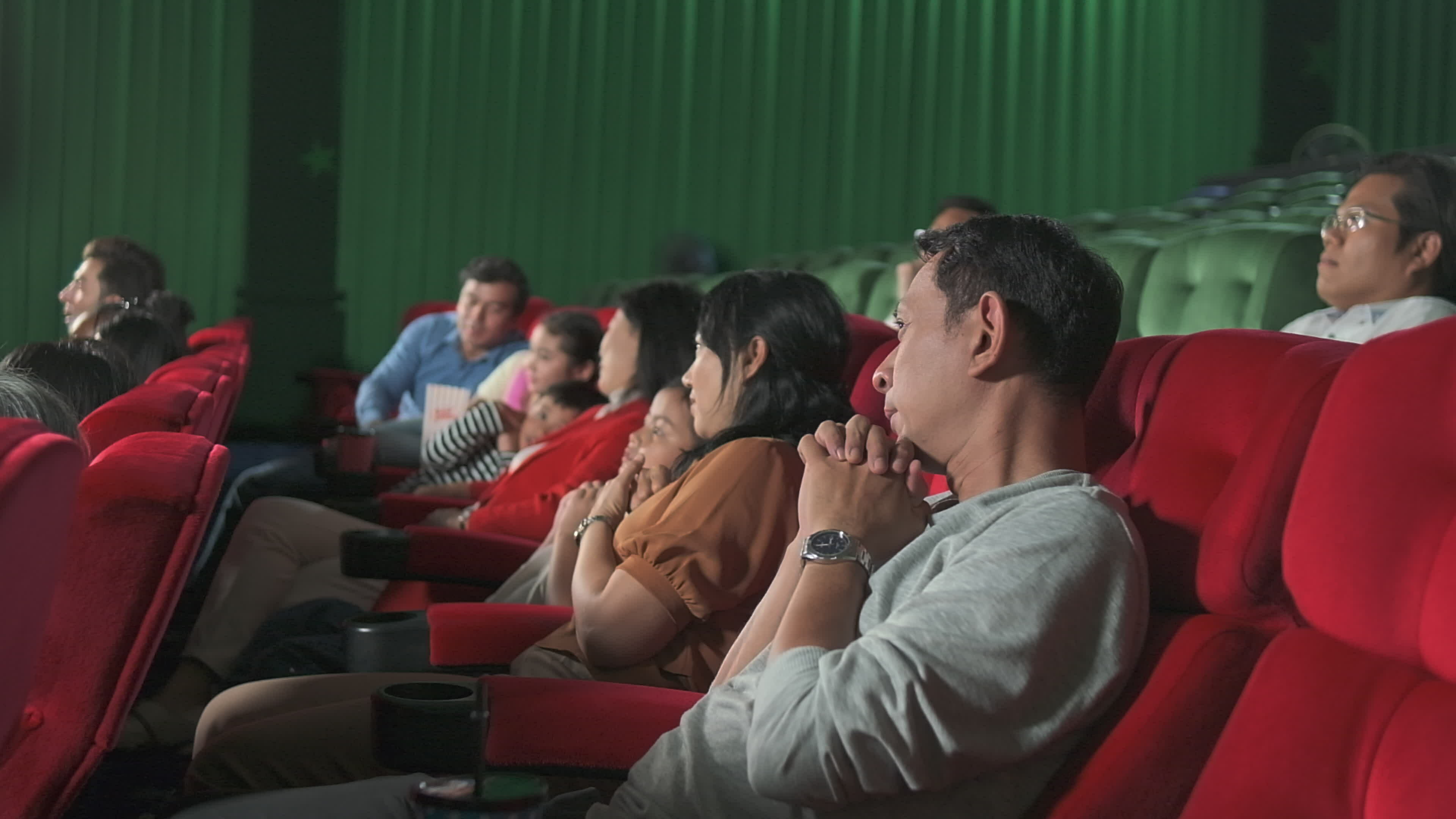 Various people in theater. Asian family and other audiences are scared of watching thriller and ...