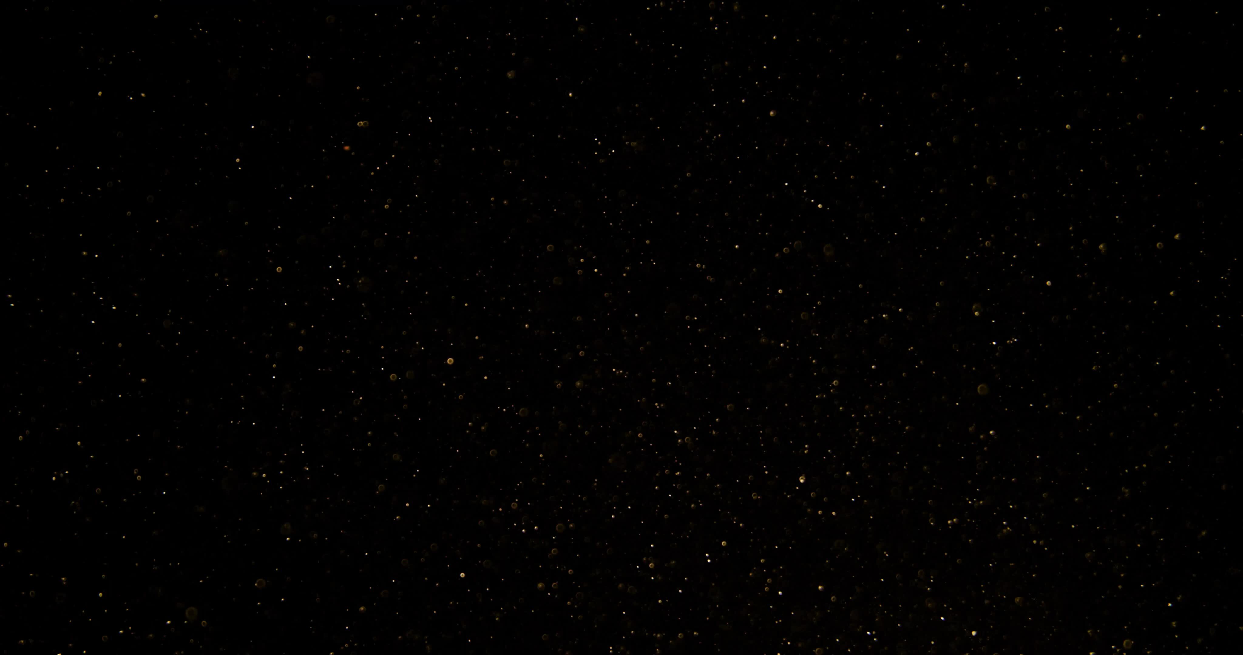 Cinematic warm dust particles floating on black background in slow motion. Atmosphere overlay ...