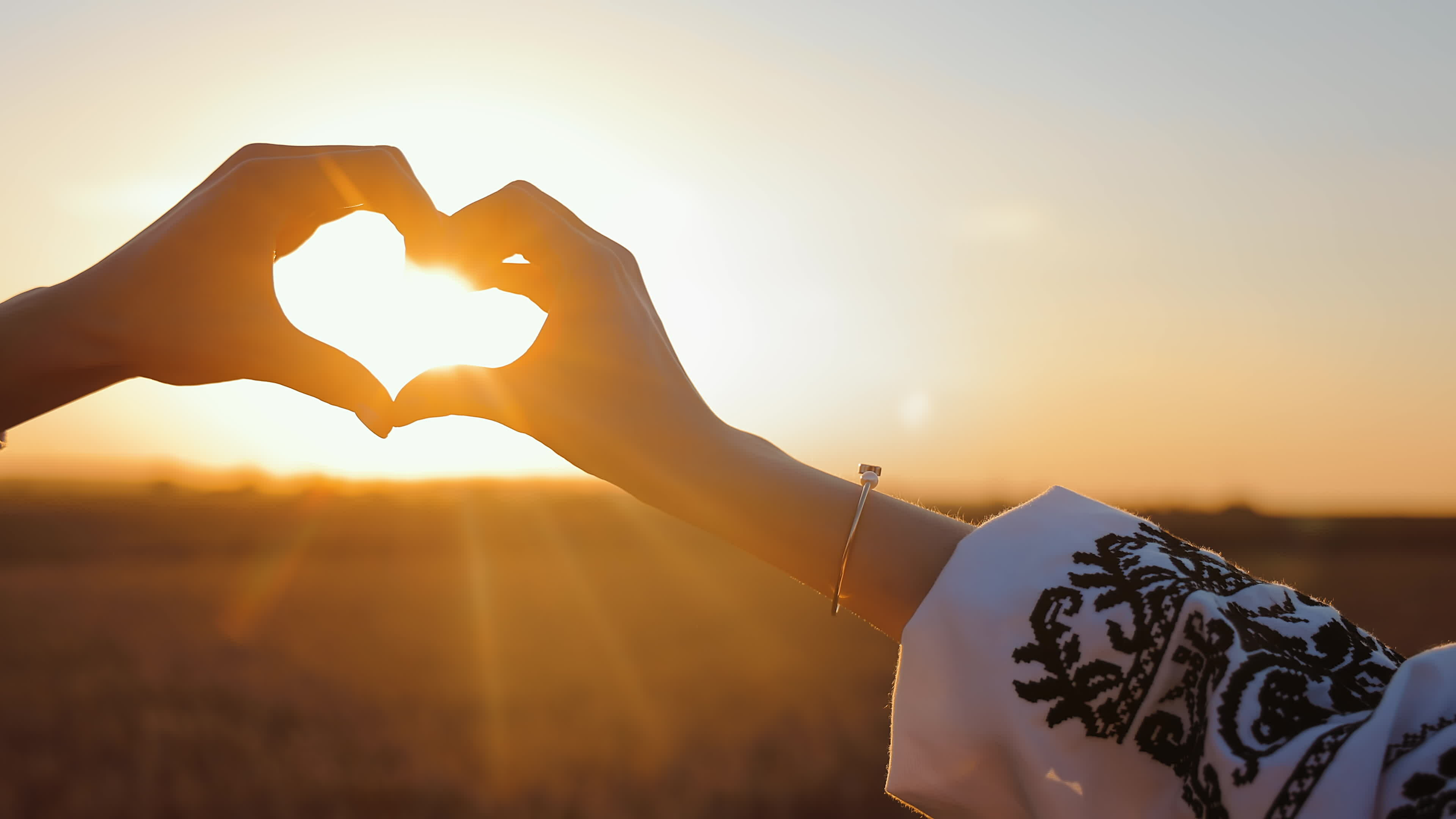 Female hands forming a heart on the background of the sunset. Fingers in the shape of a heart in ...