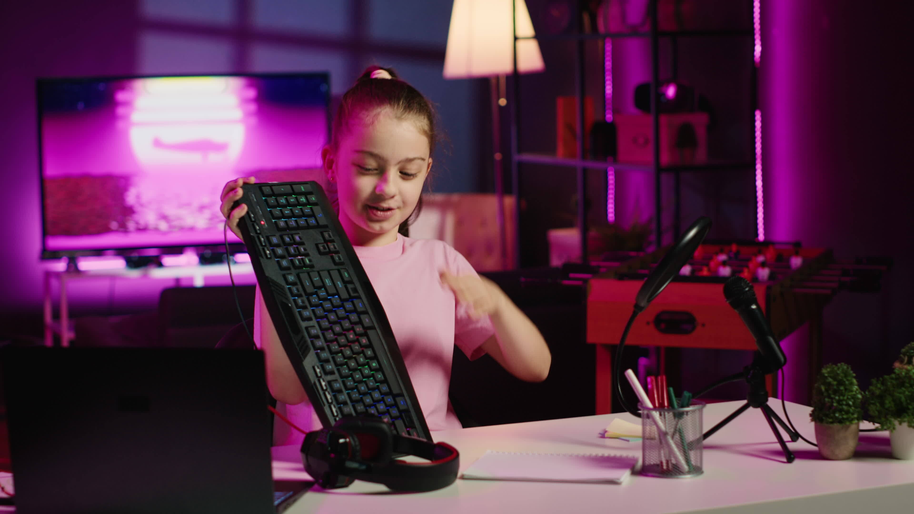 Cute girl in studio using camera to review gaming keyboard, mouse and headphones. Joyous ...