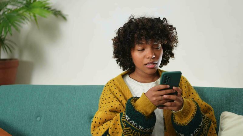 African girl holding smartphone touch screen typing scroll page at home. Woman with cell phone ...