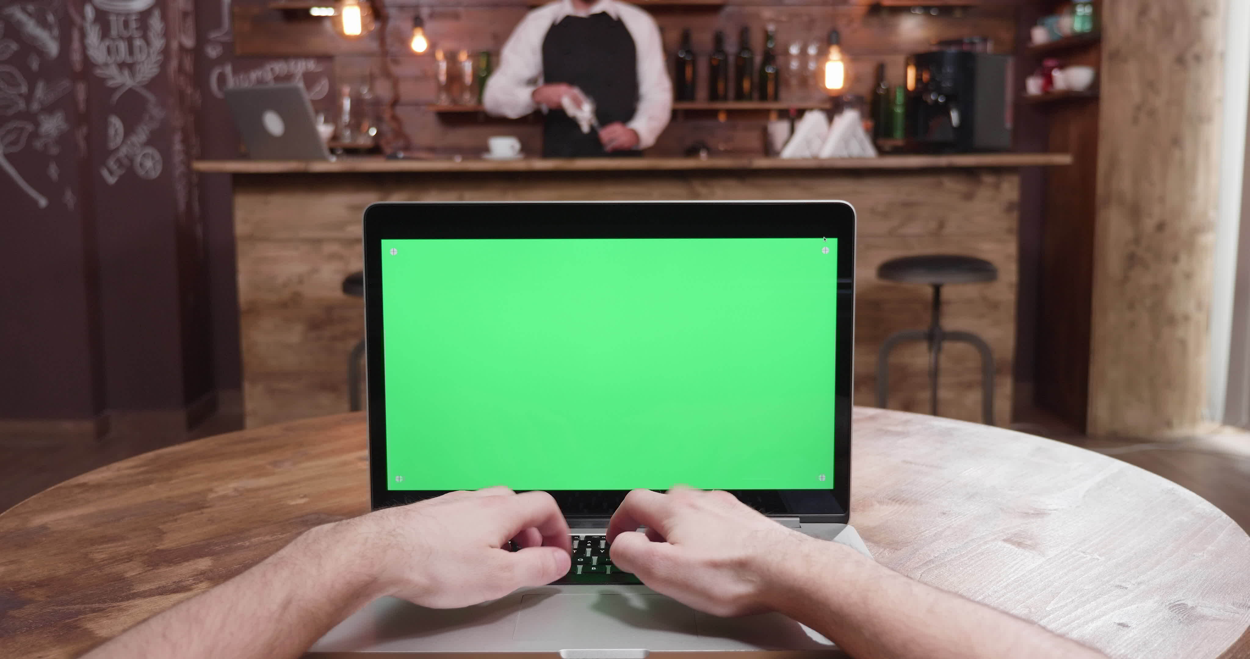 POV footage of male hands typing on computer with green screen display in a vintage cozy cafe ...