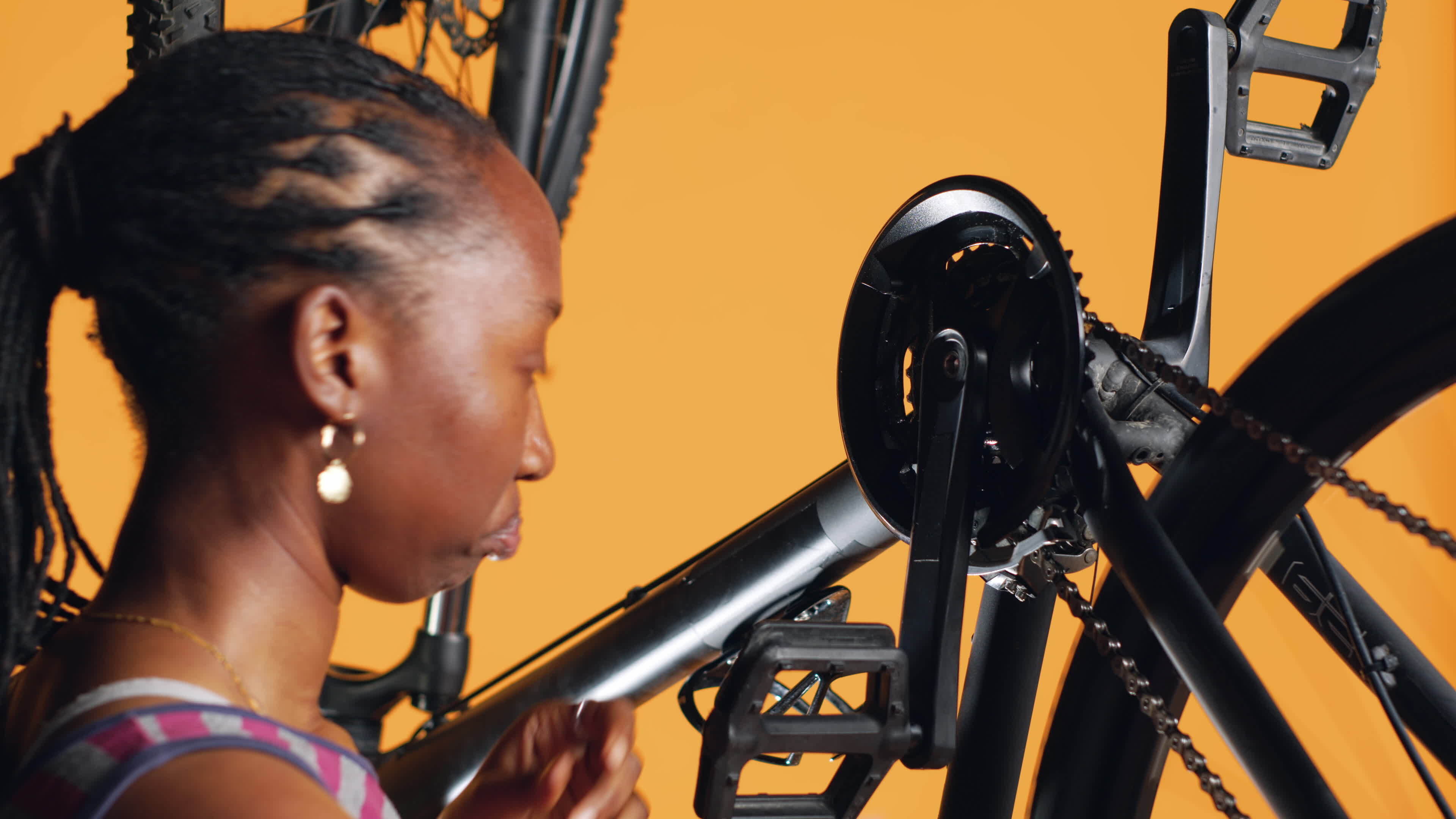 African american woman pushing pedals to spin bike wheel, inspecting it, using screwdriver and ...