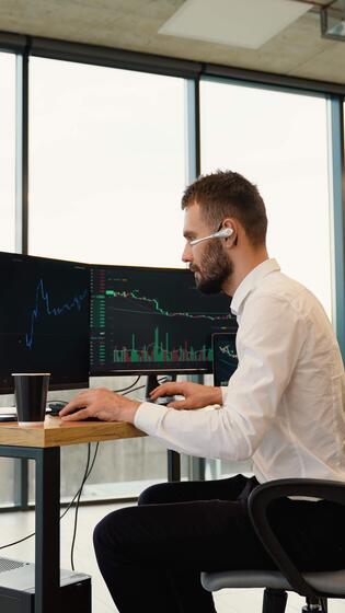 Concentrated trader sitting in front of computers, making professional analysis of candlestick ...