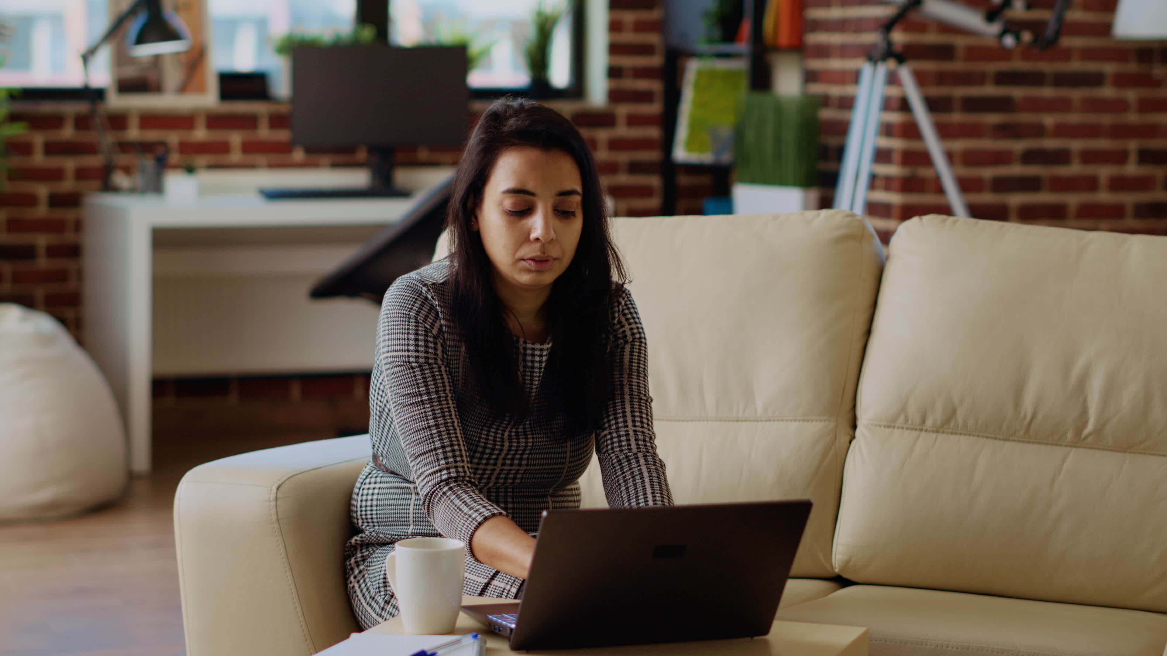 Portrait of upbeat teleworker sitting on couch, remotely performing tasks in personal office ...