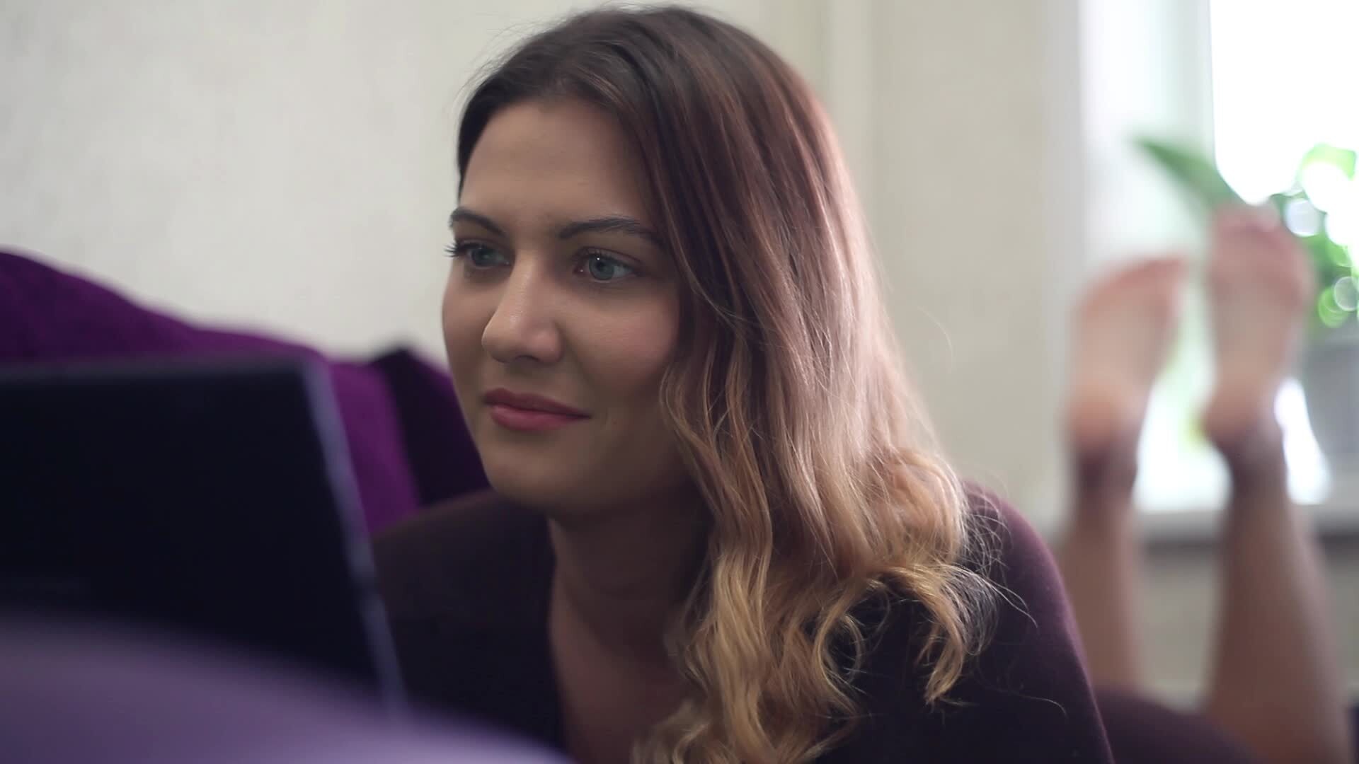 Close-up. Beautiful young girl with long hair enjoys a tablet lying on a diman and smiles ...