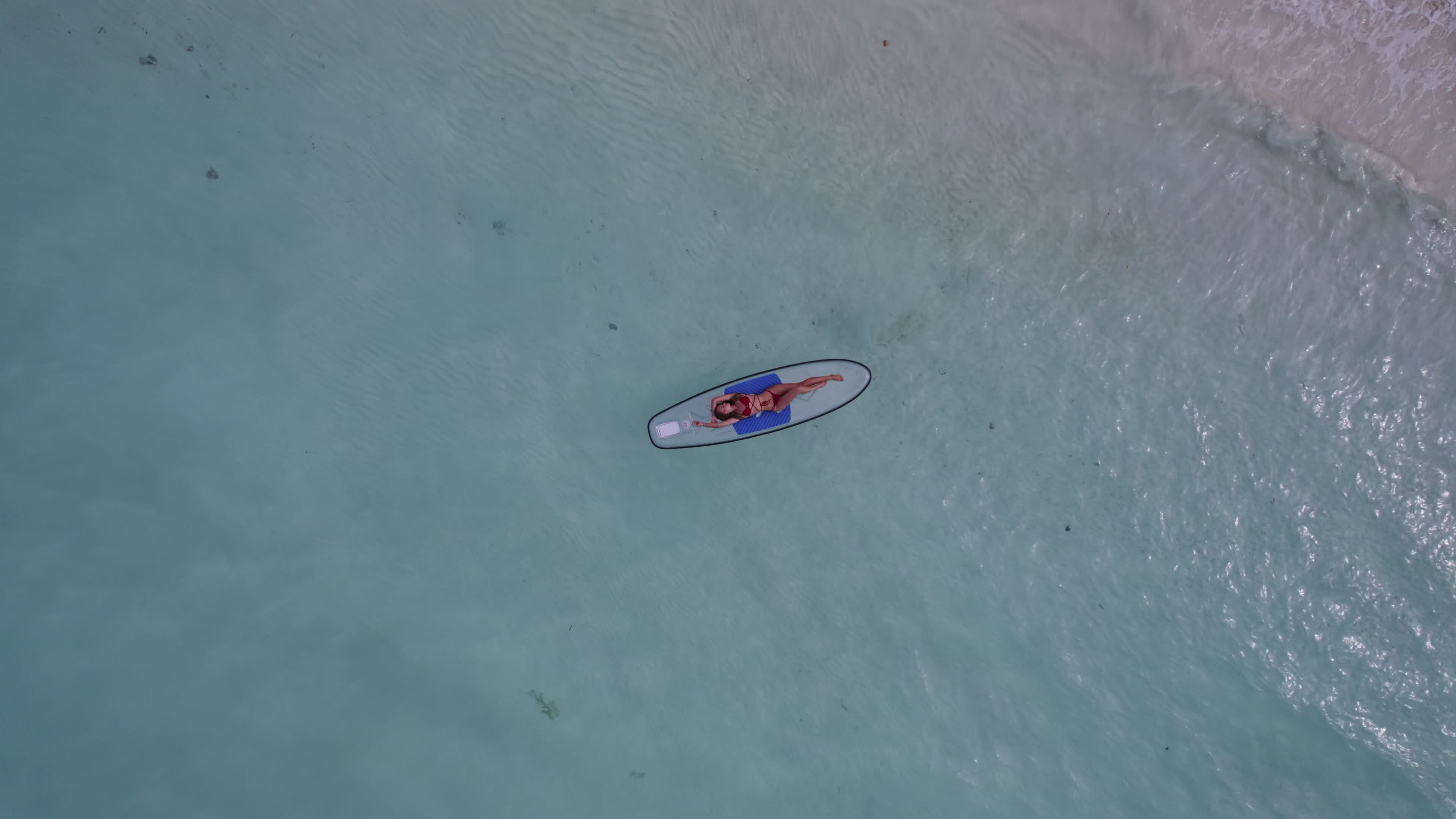A girl is lying on a paddleboard in the ocean. The camera goes up ...