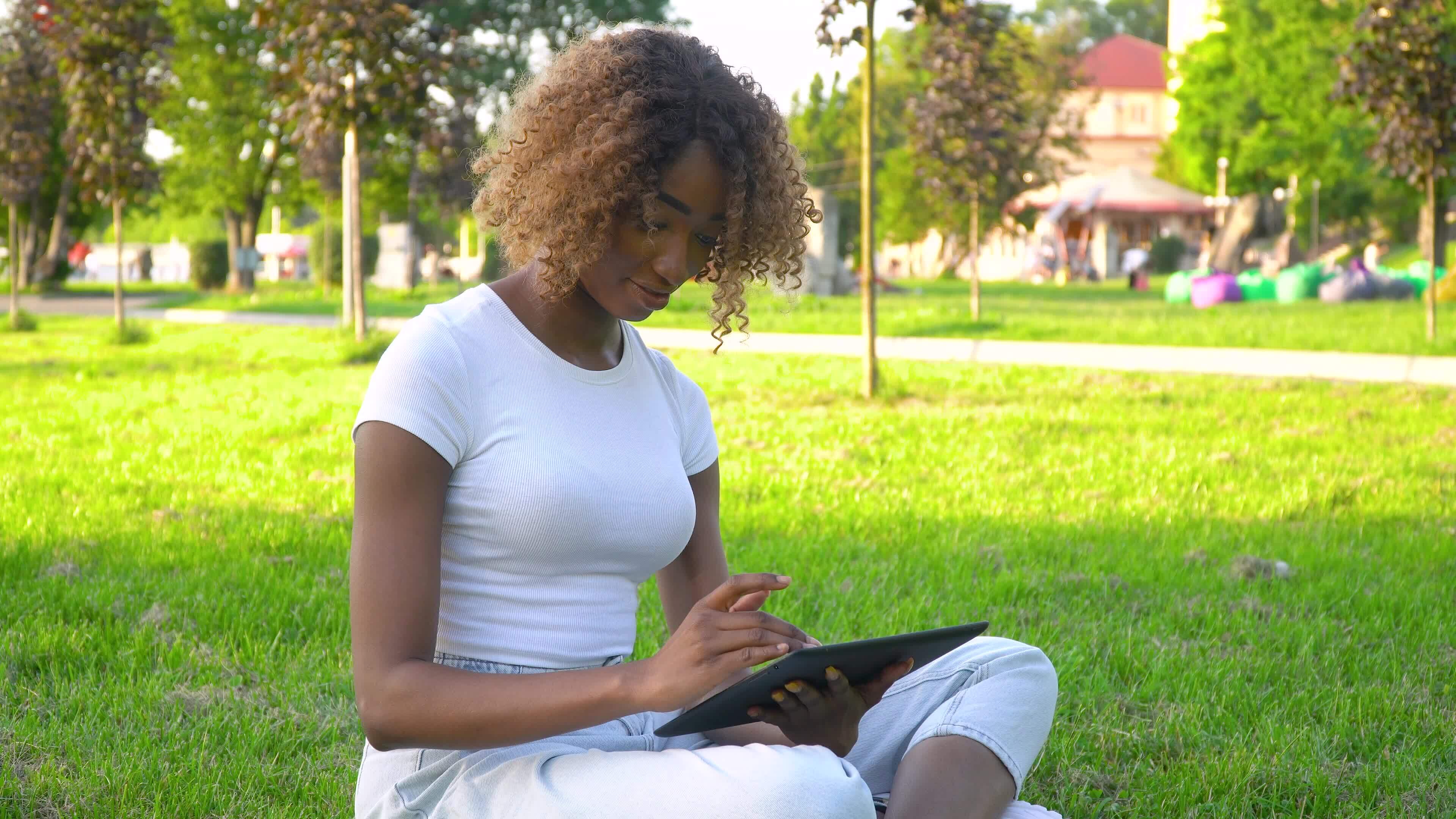 Young african american woman using tablet in park. Online learning ...
