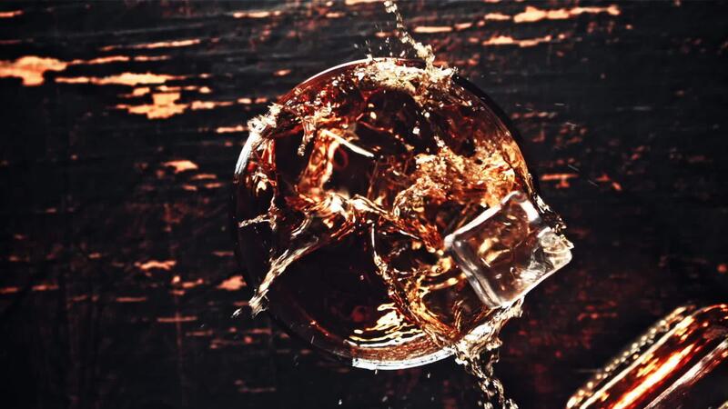 Ice with splashes falls into a glass of whiskey. Top view. Against a dark background.Filmed on a ...