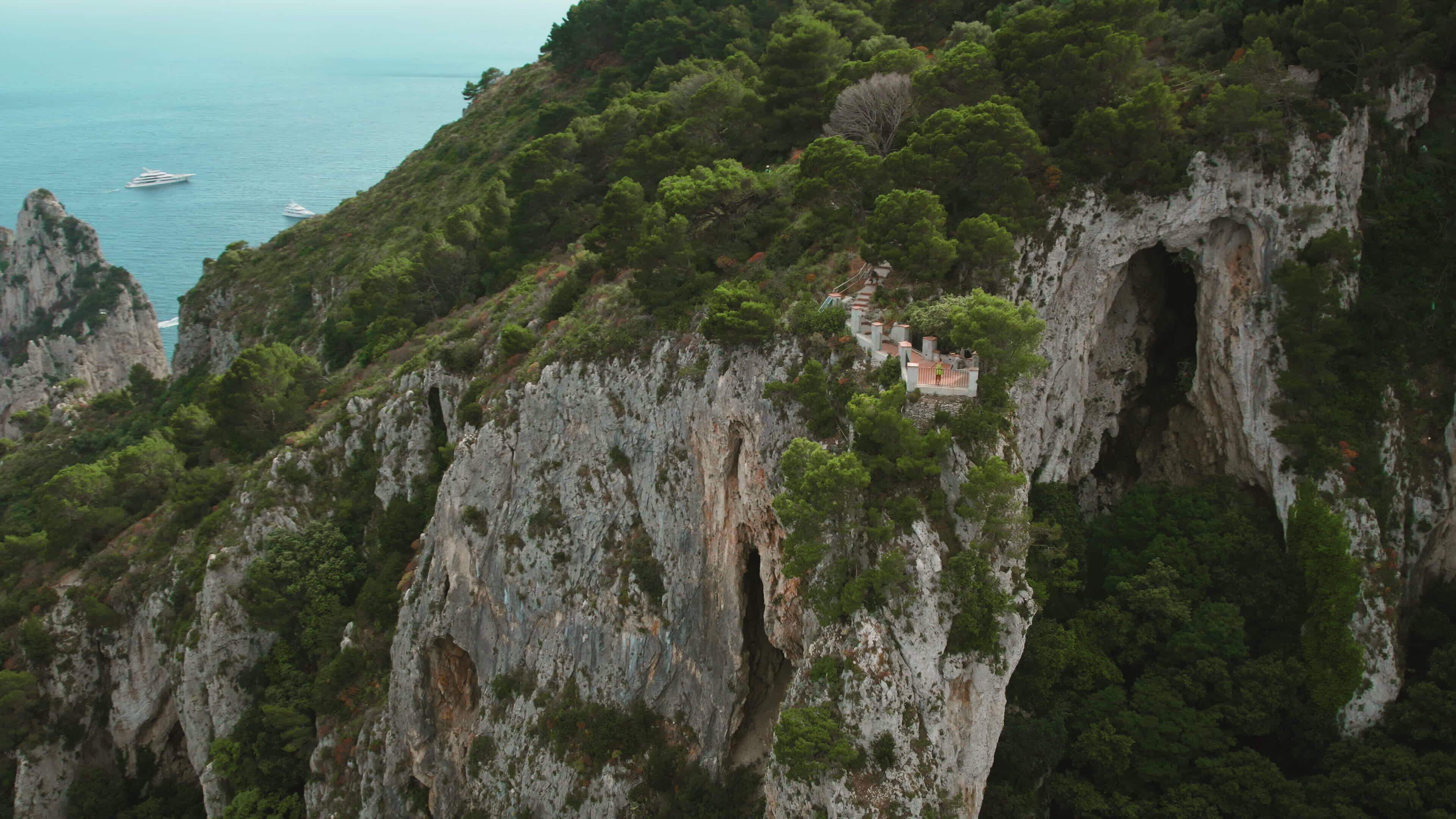 Majestic cliffs tower over tranquil azure sea waters. Woman on viewpoint overlooking Capri ...