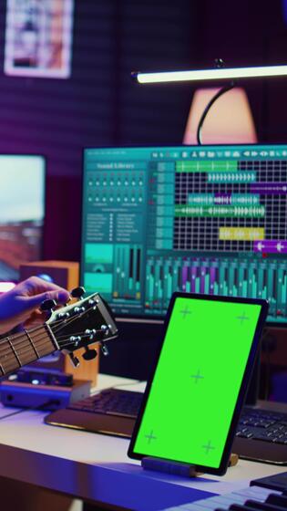 Vertical Video Audio engineer practices tuning his acoustic guitar in home studio, watching a ...