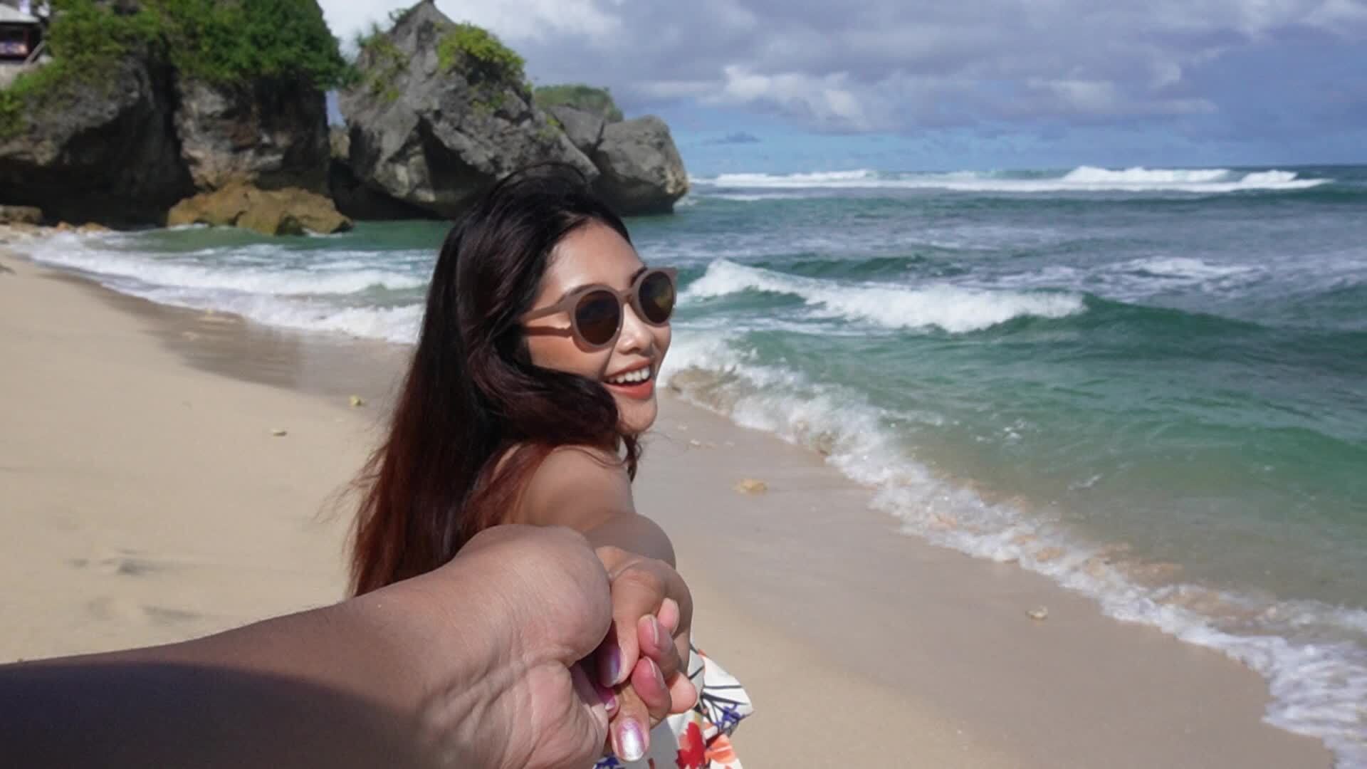 POV of happy smiling woman on summer vacation at a beach. Female traveler holding hands and ...
