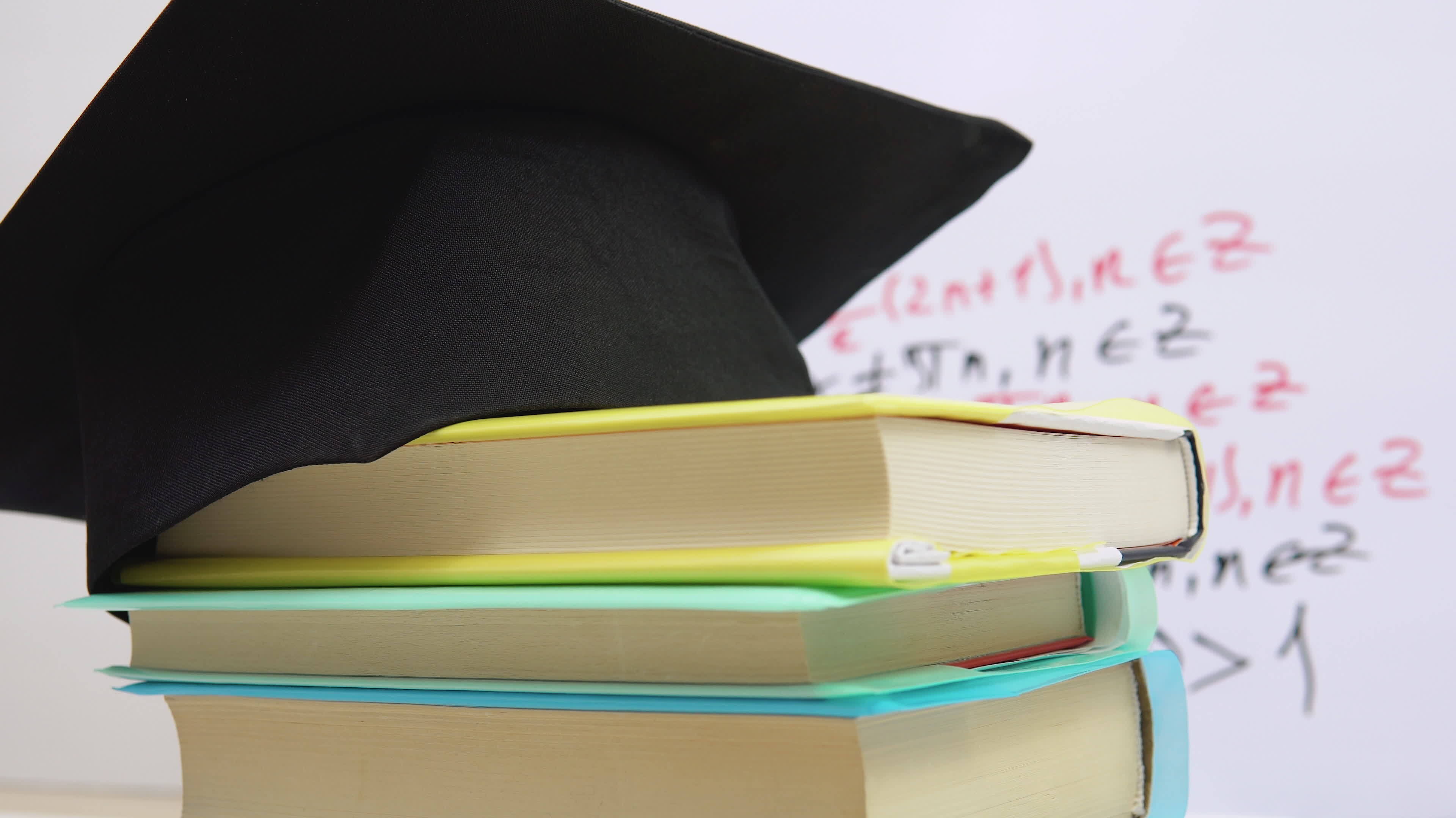 The black square hat of the master lies on the textbooks stacked in a ... The black square hat of the master lies on the textbooks stacked in a ...