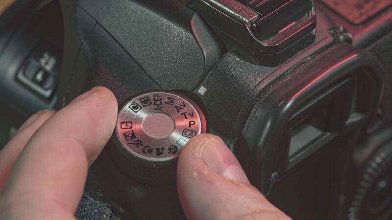 Man turning Canon DSLR camera settings mode dial wheel to the M manual mode from the full ...