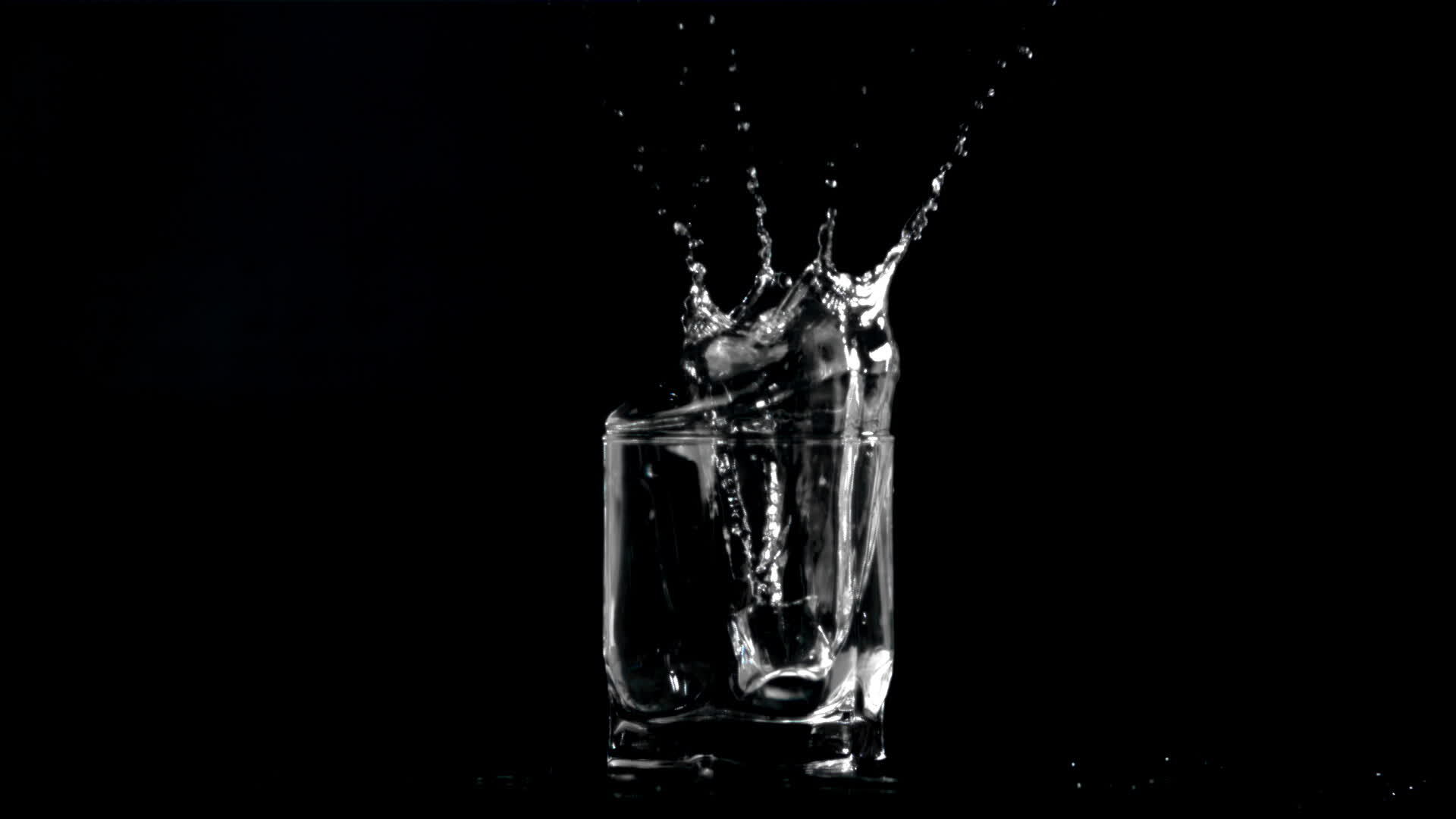 Super slow motion in a glass of water falls ice cube with spray. Filmed at 1000 fps.On a black ...