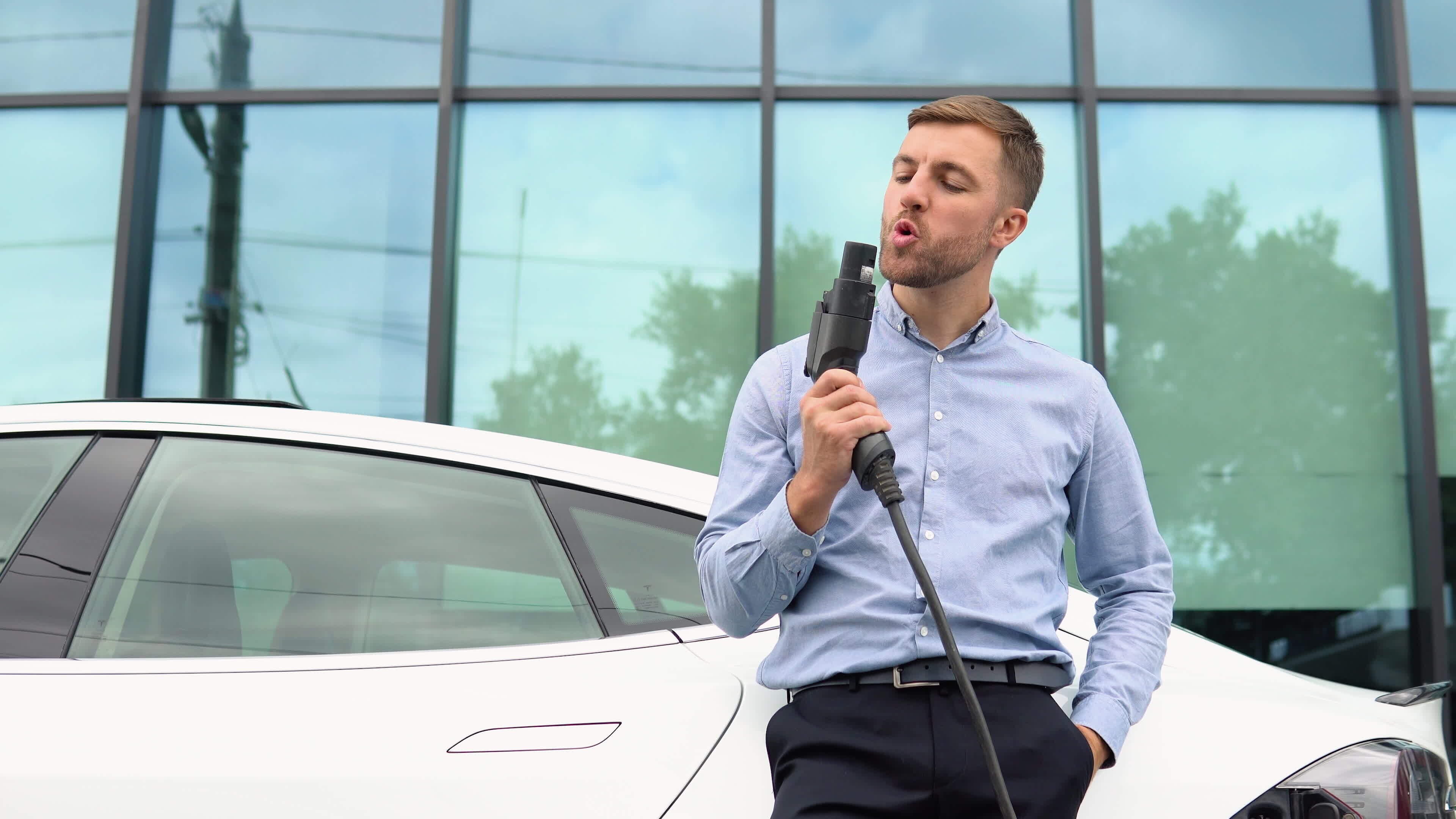Hansome Guy Standing Near His New Modern Electric Car And Holding Plug Of The Charger 43792014