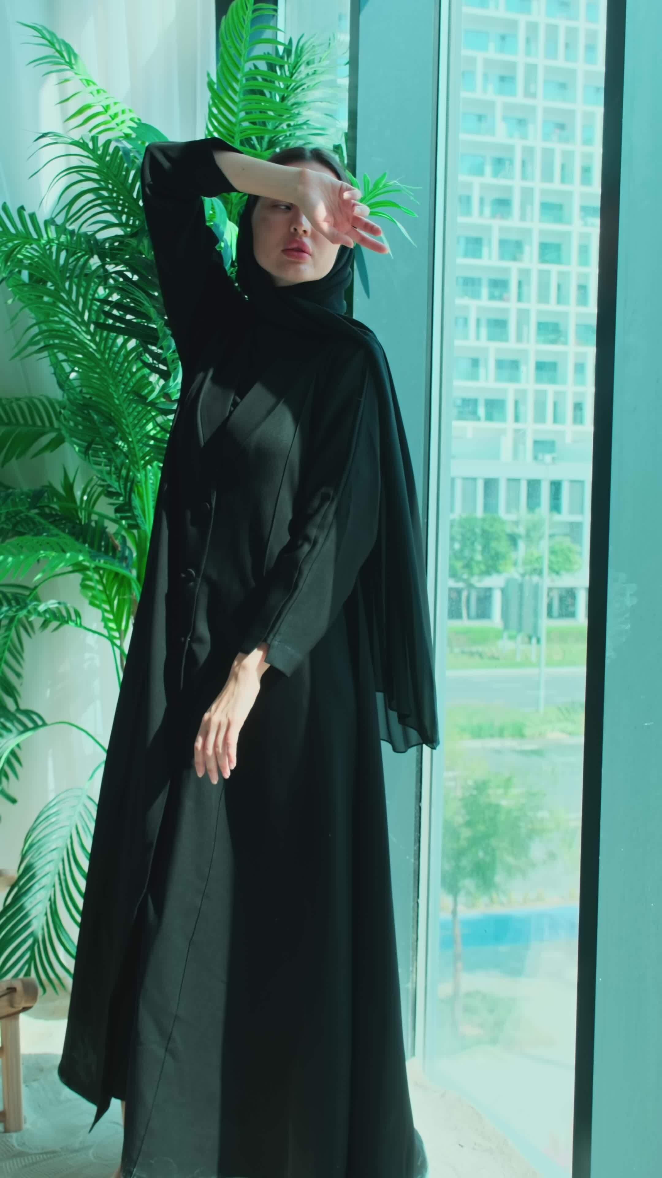 A young woman in the Arab national dress of the abaya is dancing near window. Close-up of dress ...