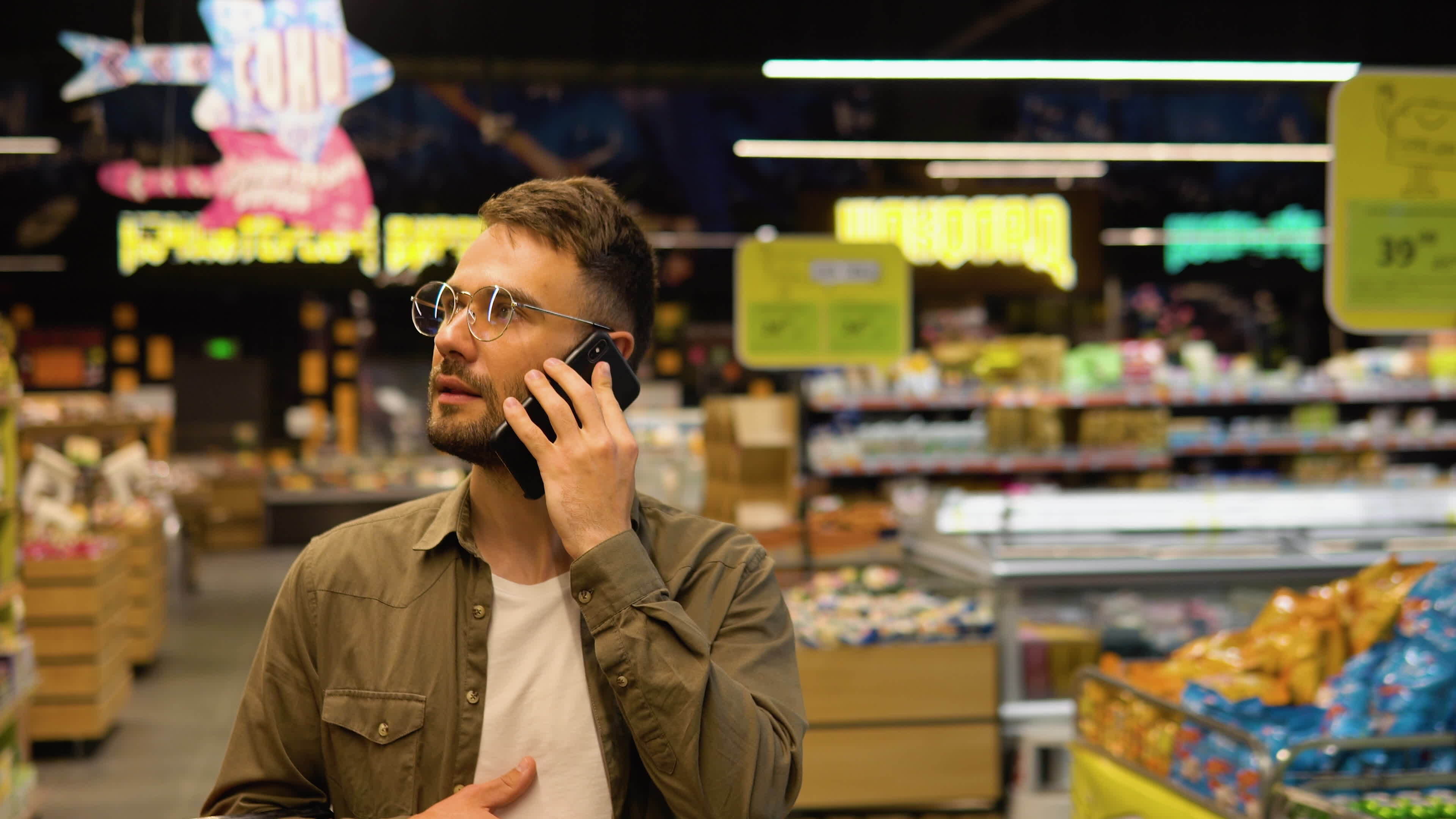 Young man walks in a supermarket makes purchases, chooses products and talks on the phone ...