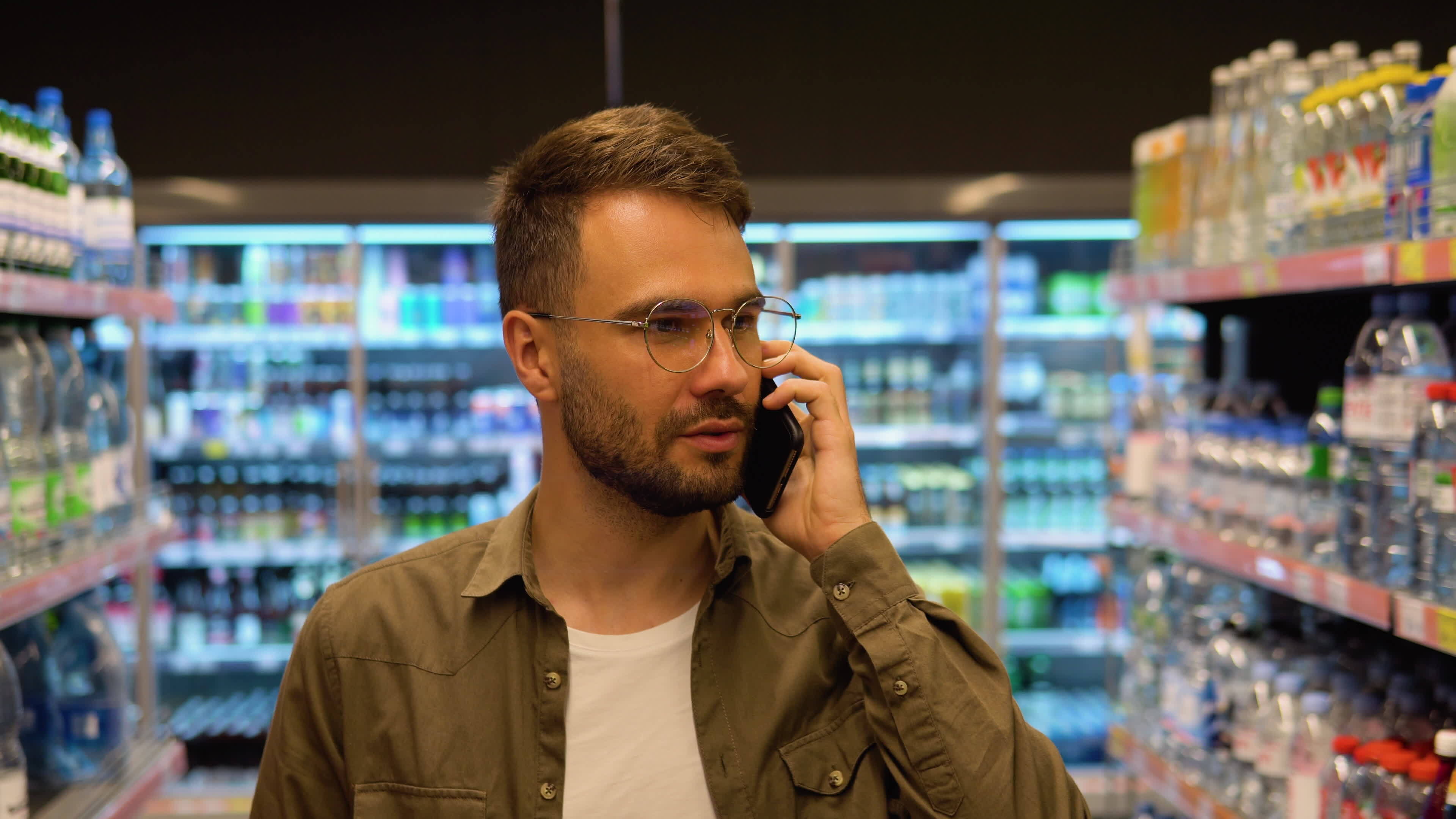 Young man walks in a supermarket makes purchases, chooses products and talks on the phone ...