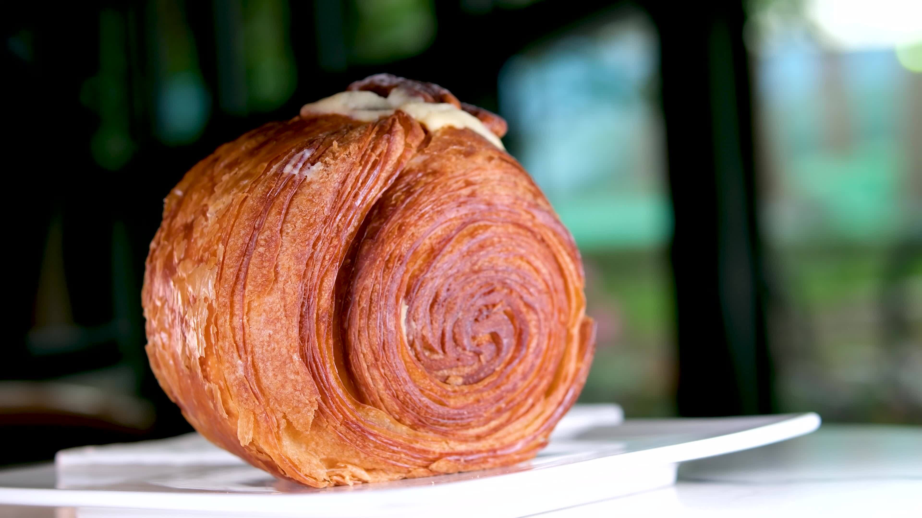 Artisan baker finishes off round buttery almond croissant by gently placing top shell on piped ...