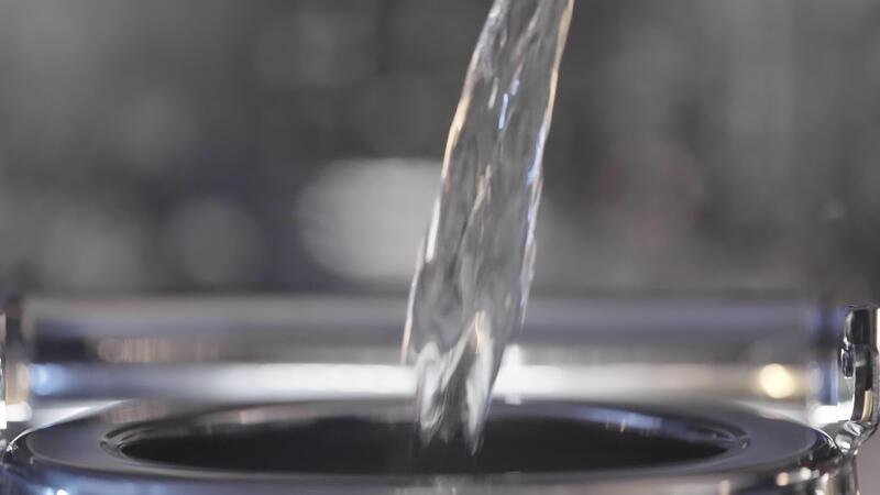 Close-up of water being poured into metal kettle. Action. Stream of clean water is poured into ...