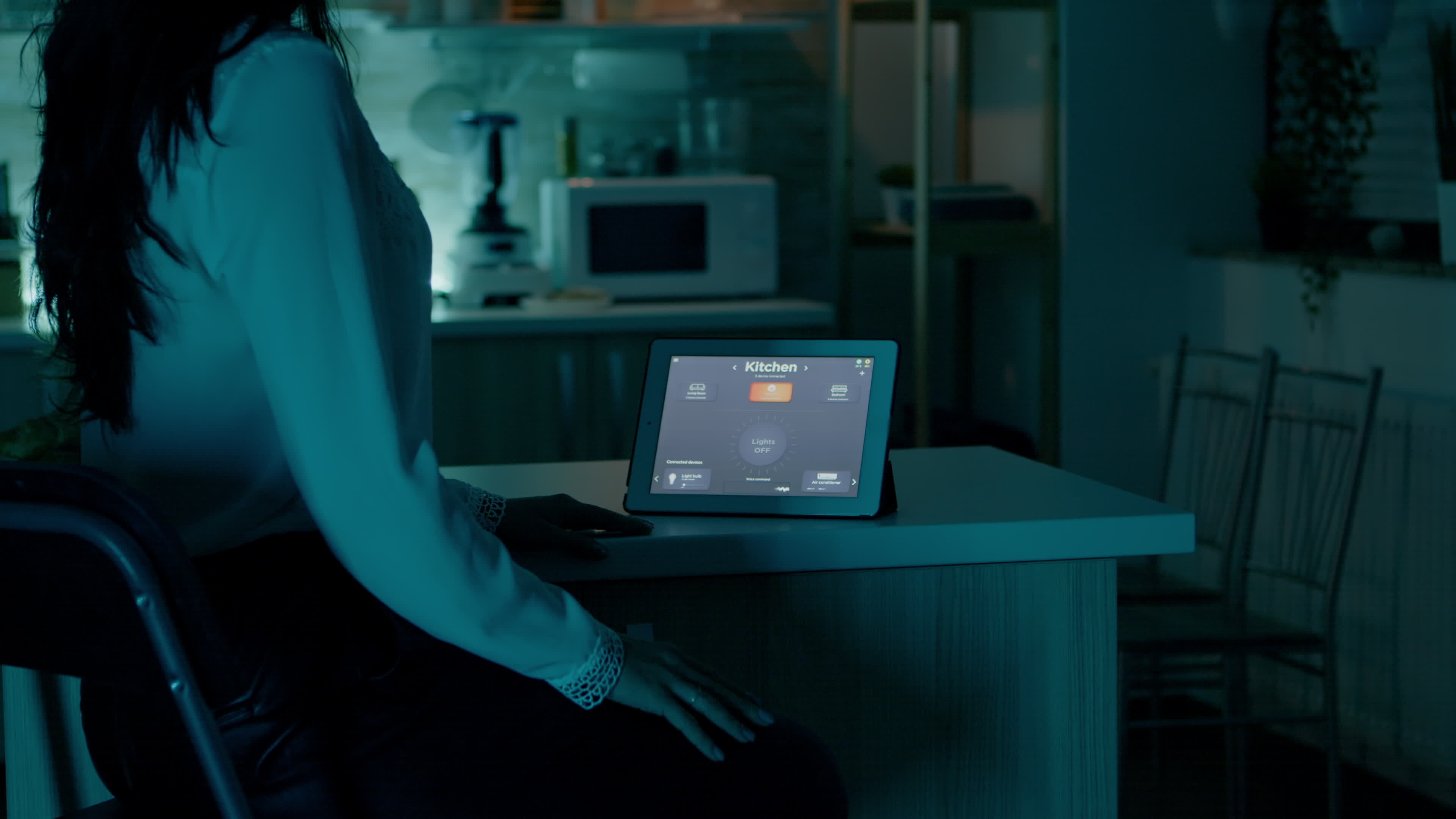 Woman Looking At Tablet In House With Automation Lighting System Sitting In Kitchen Switching