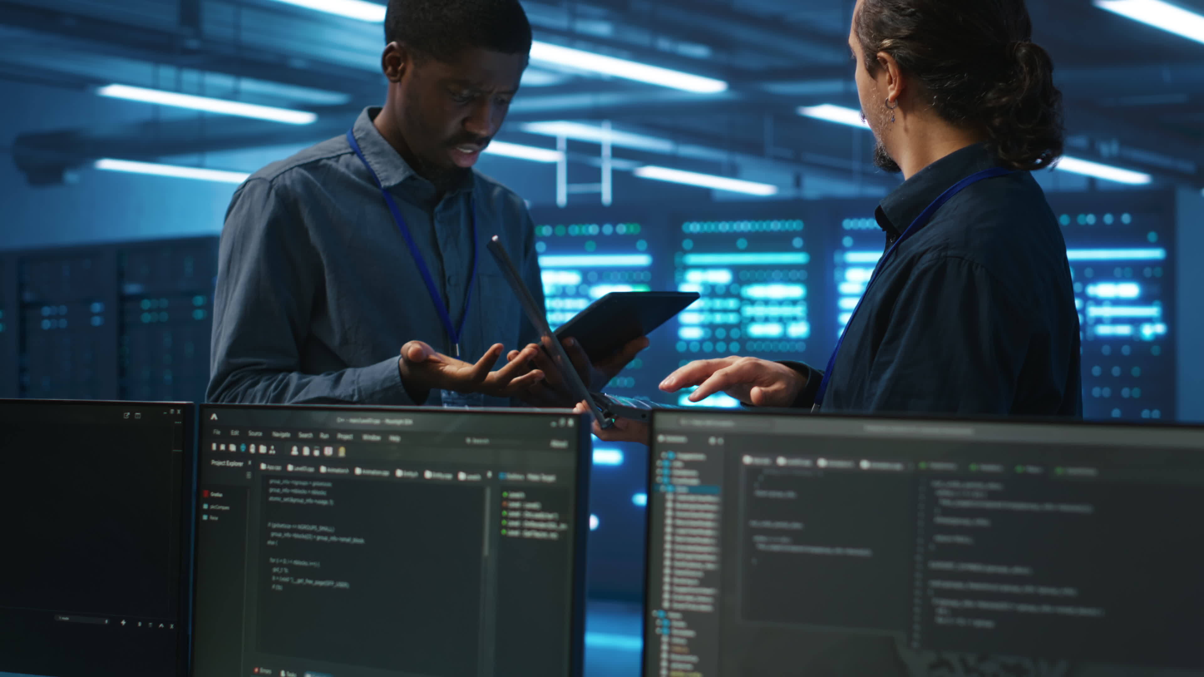 Engineers working in high tech server farm, using laptop and tablet to analyze data, ensuring ...